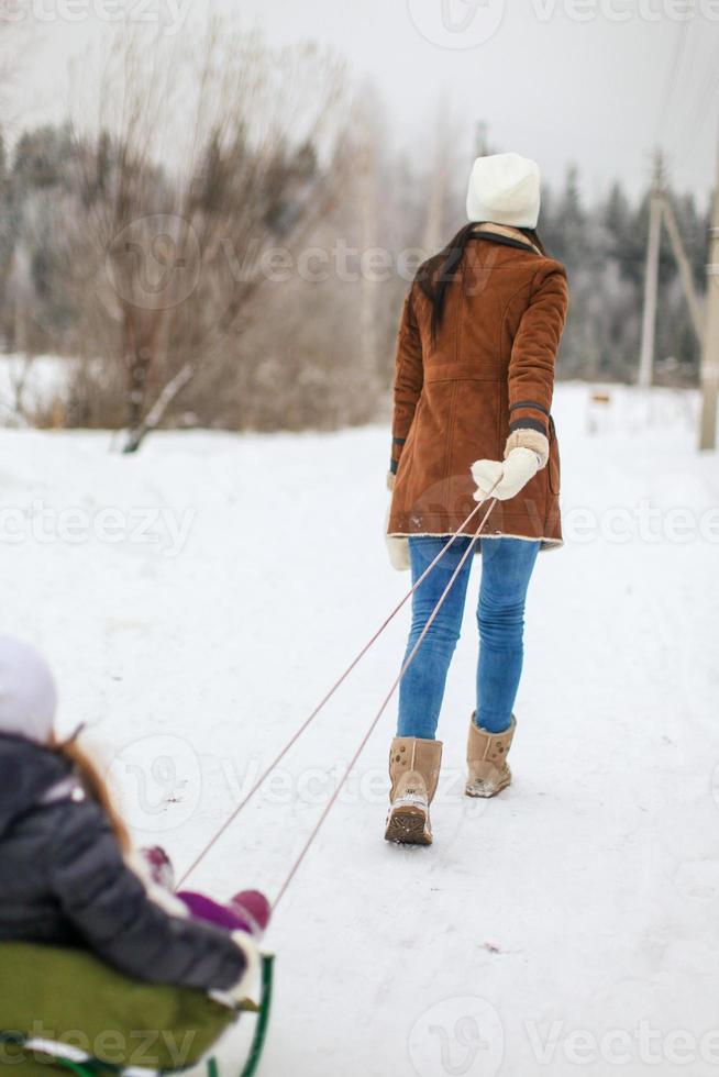 Rear view of Young mother rolls her little cute daughters on a sled in ... Rear view of Young mother rolls her little cute daughters on a sled in ...