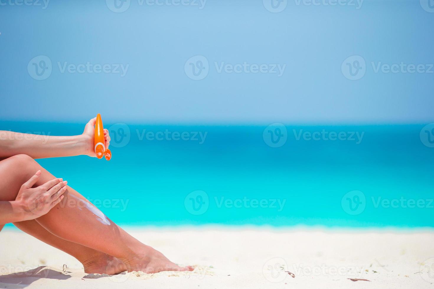 Slim Woman Applying Sunscreen On Her Legs Sitting On Sandy Beach With