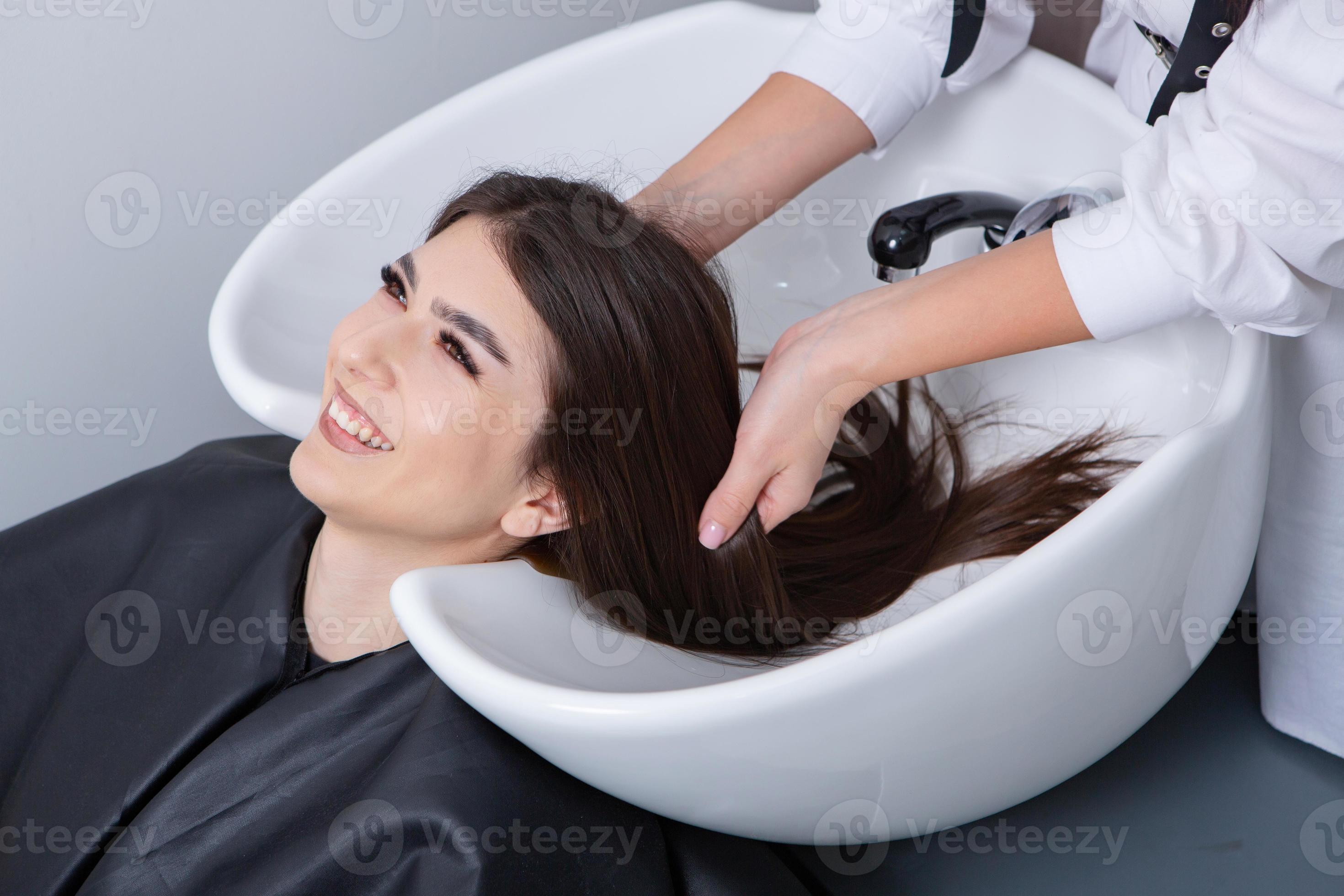 professional hairdresser washing hair of young woman in beauty salon. close up of woman's hair ...