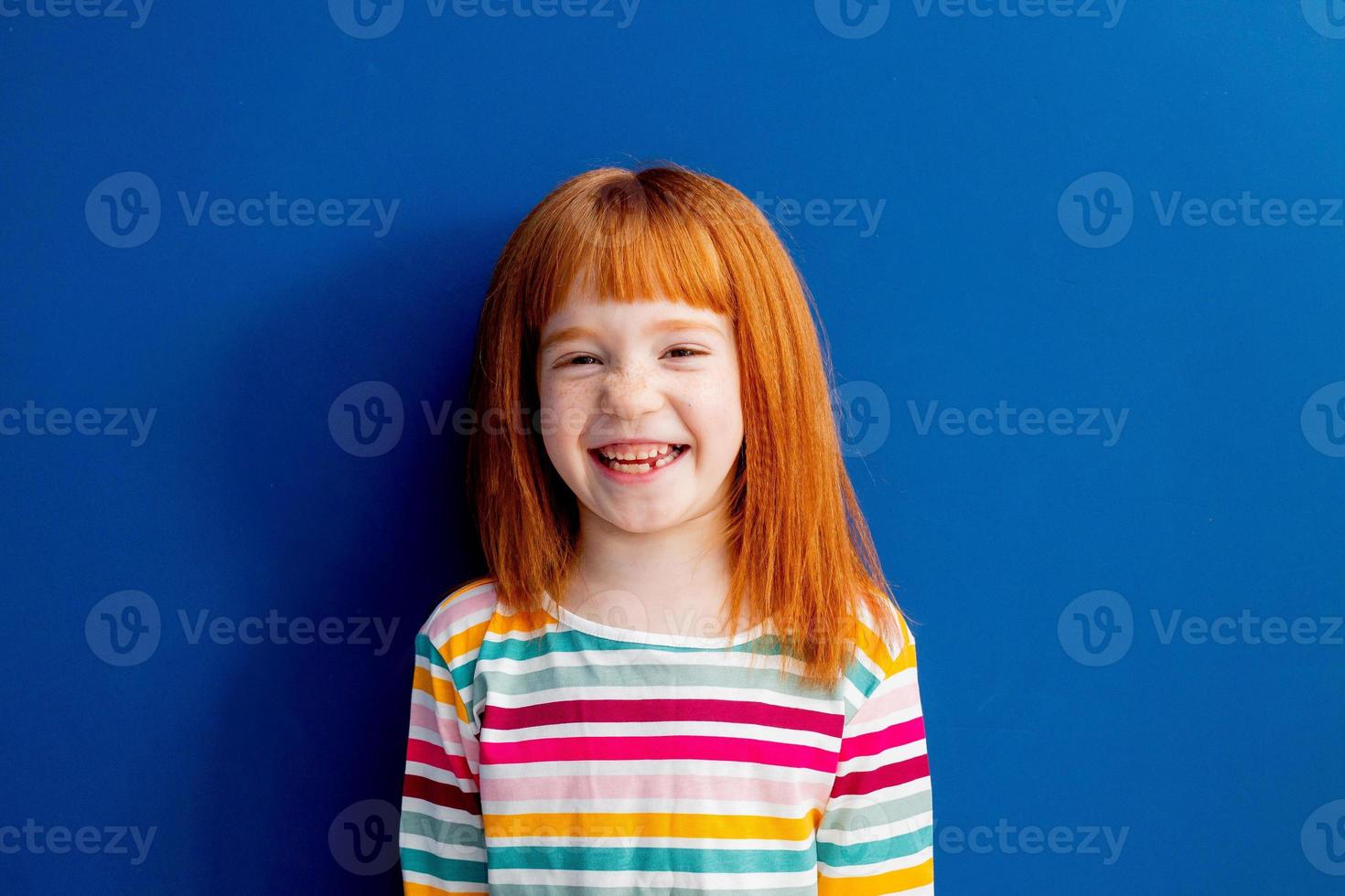 little girl with red hair in a multicolored smile stands on a blue ...