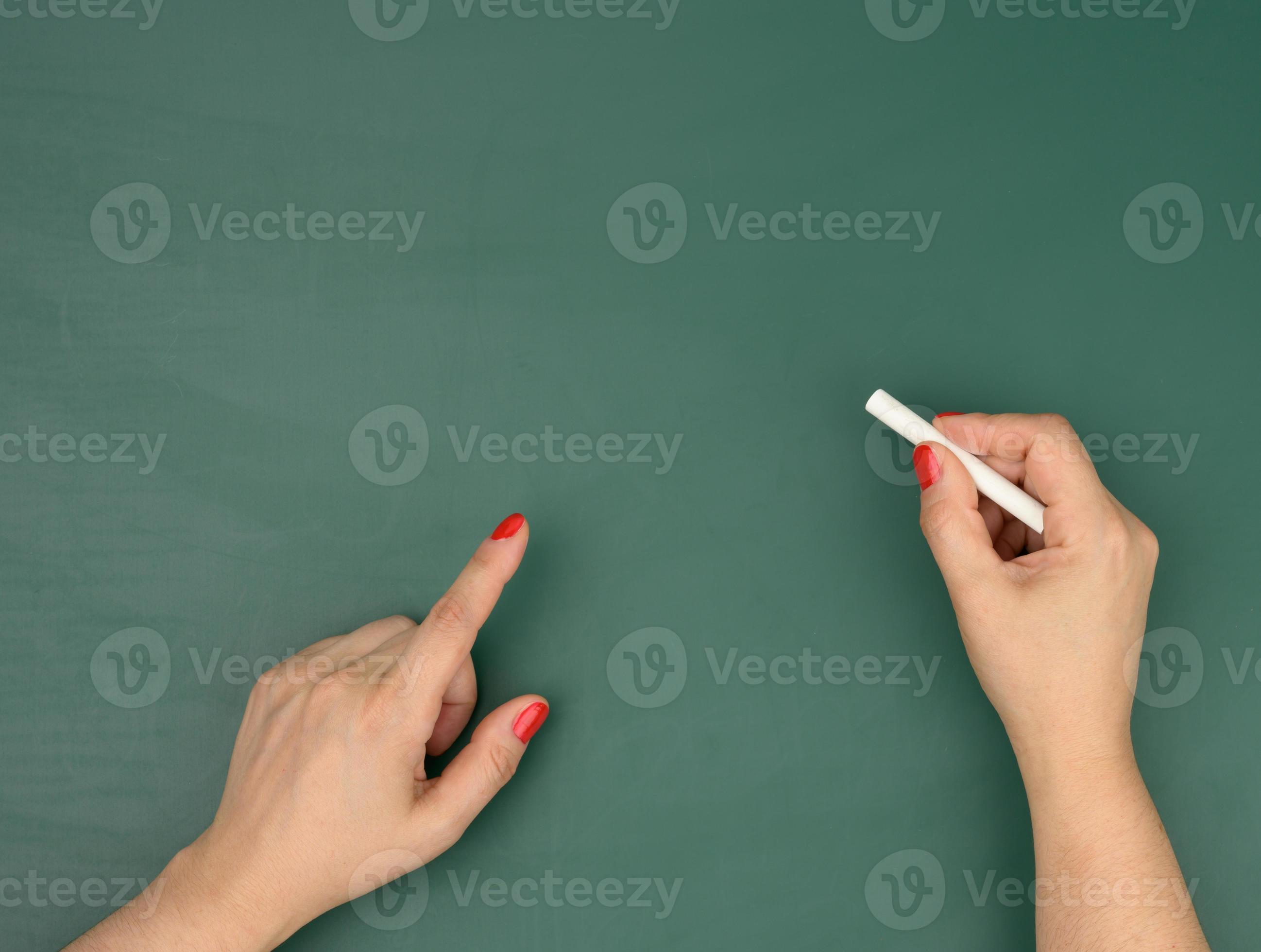 Hand Holds A Piece Of White Chalk On The Background Of An Empty Green