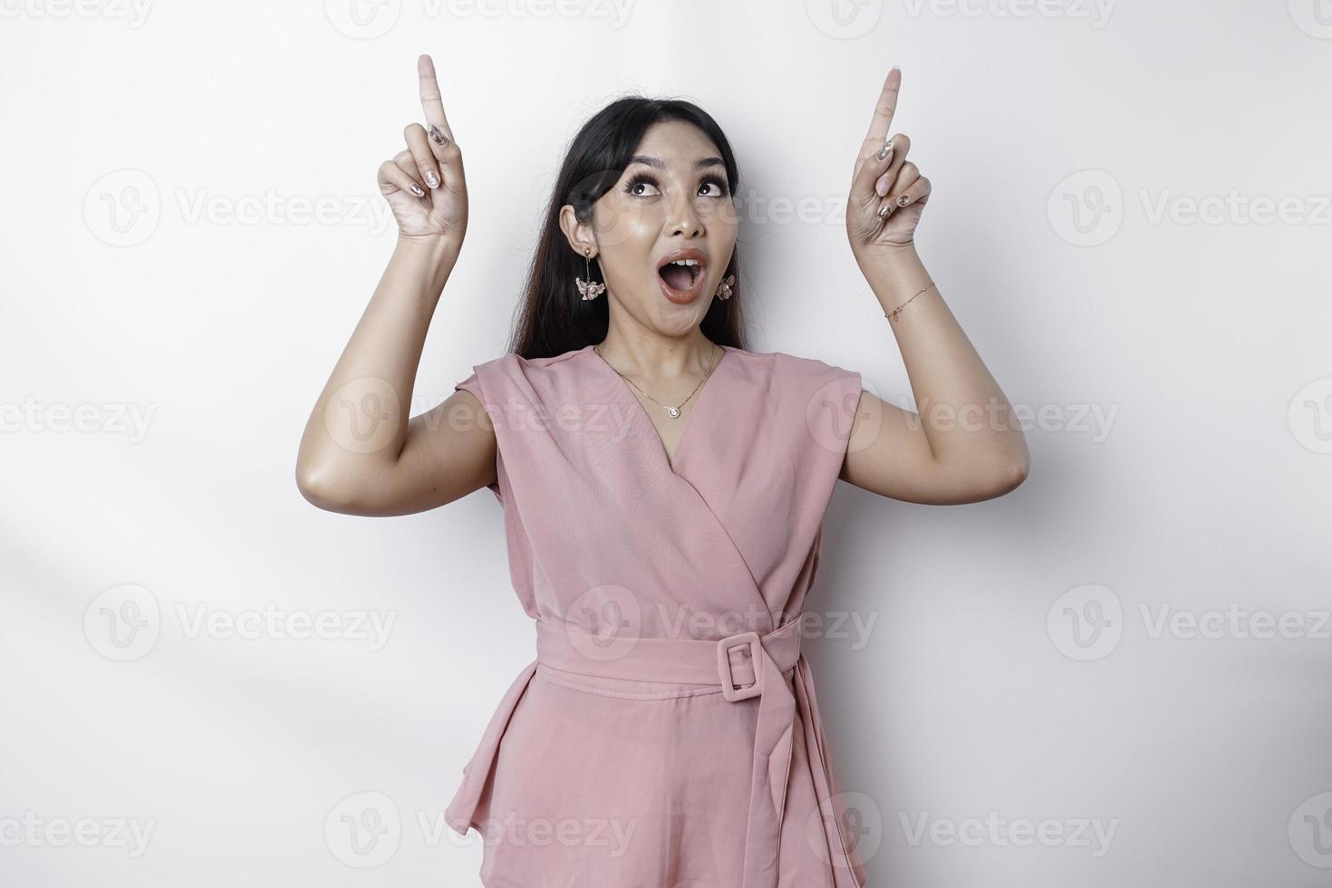 Shocked Asian woman dressed in pink, pointing at the copy space on top ...