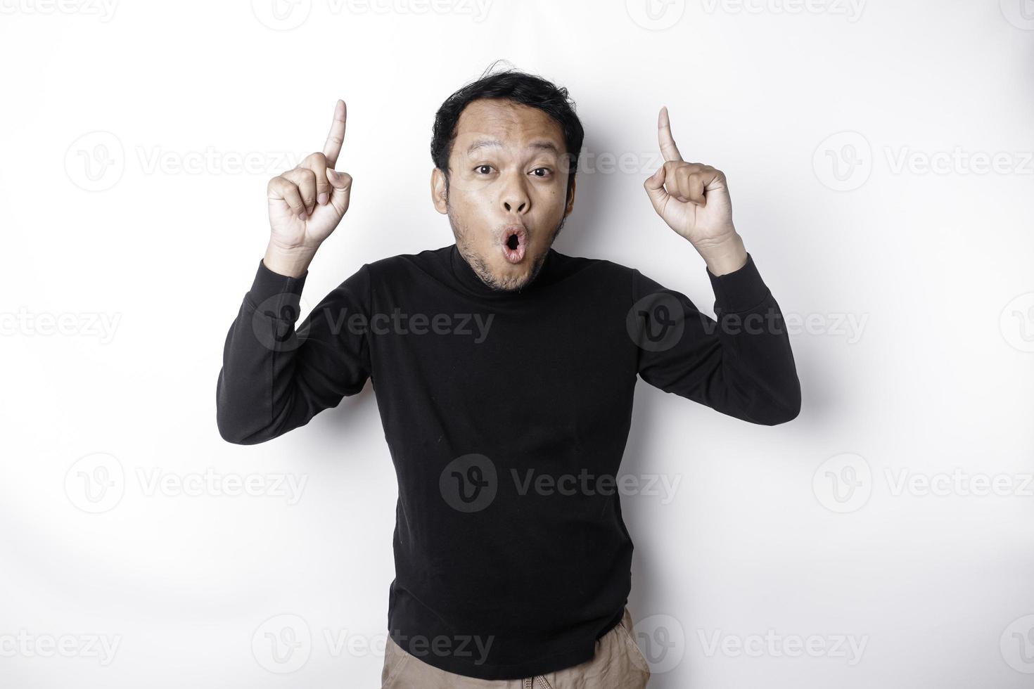 Shocked Asian man wearing black shirt pointing at the copy space on top ...