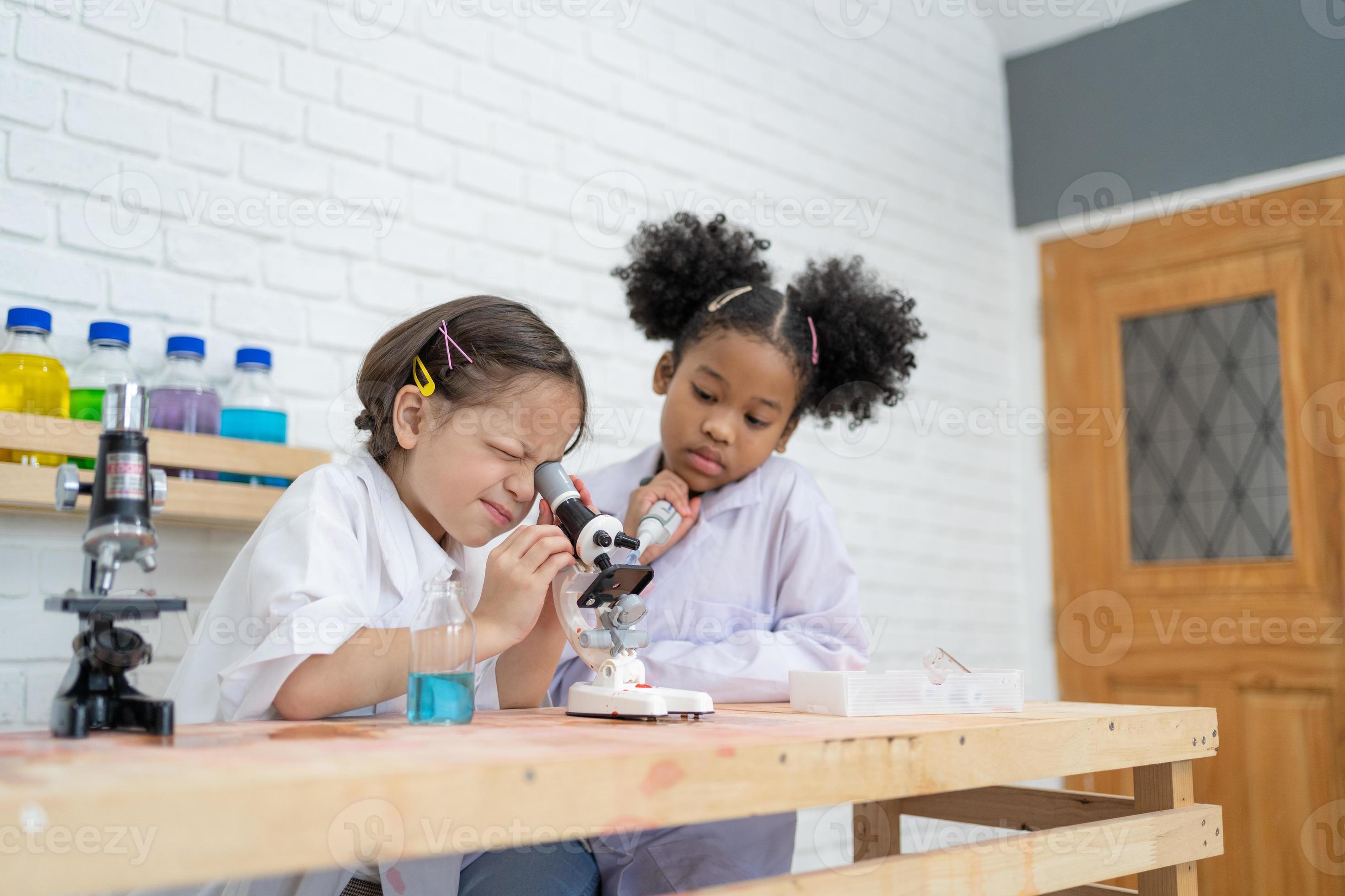 Two little kids in lab coat learning chemistry in school laboratory. Young scientists in ...