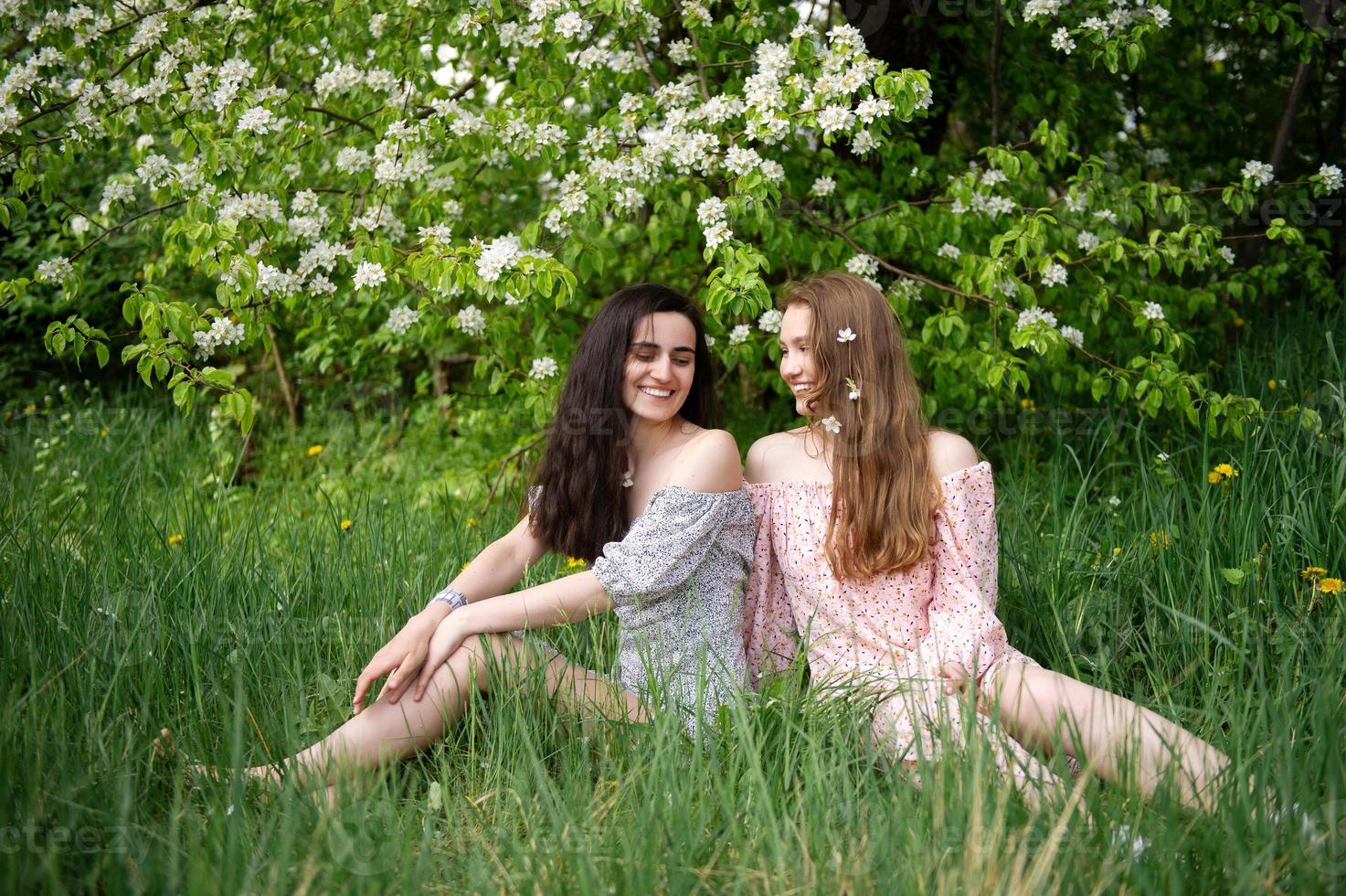 Two young girls in dresses are sitting on the green grass under a white ...