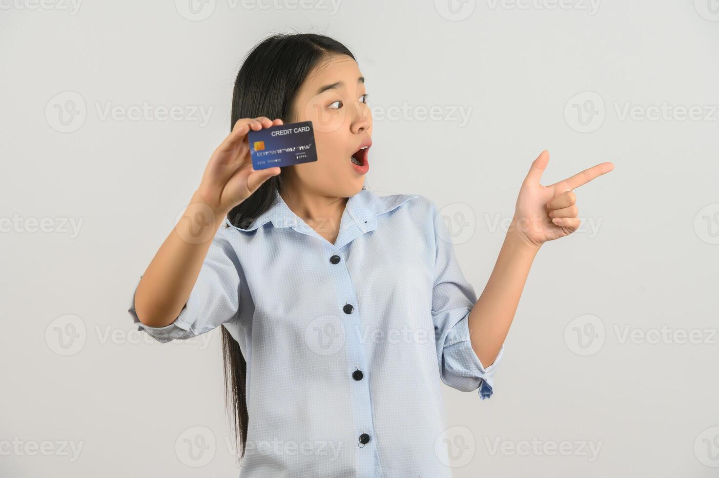 Portrait of positive young asian woman showing credit card good mood salary and pointing finger ...