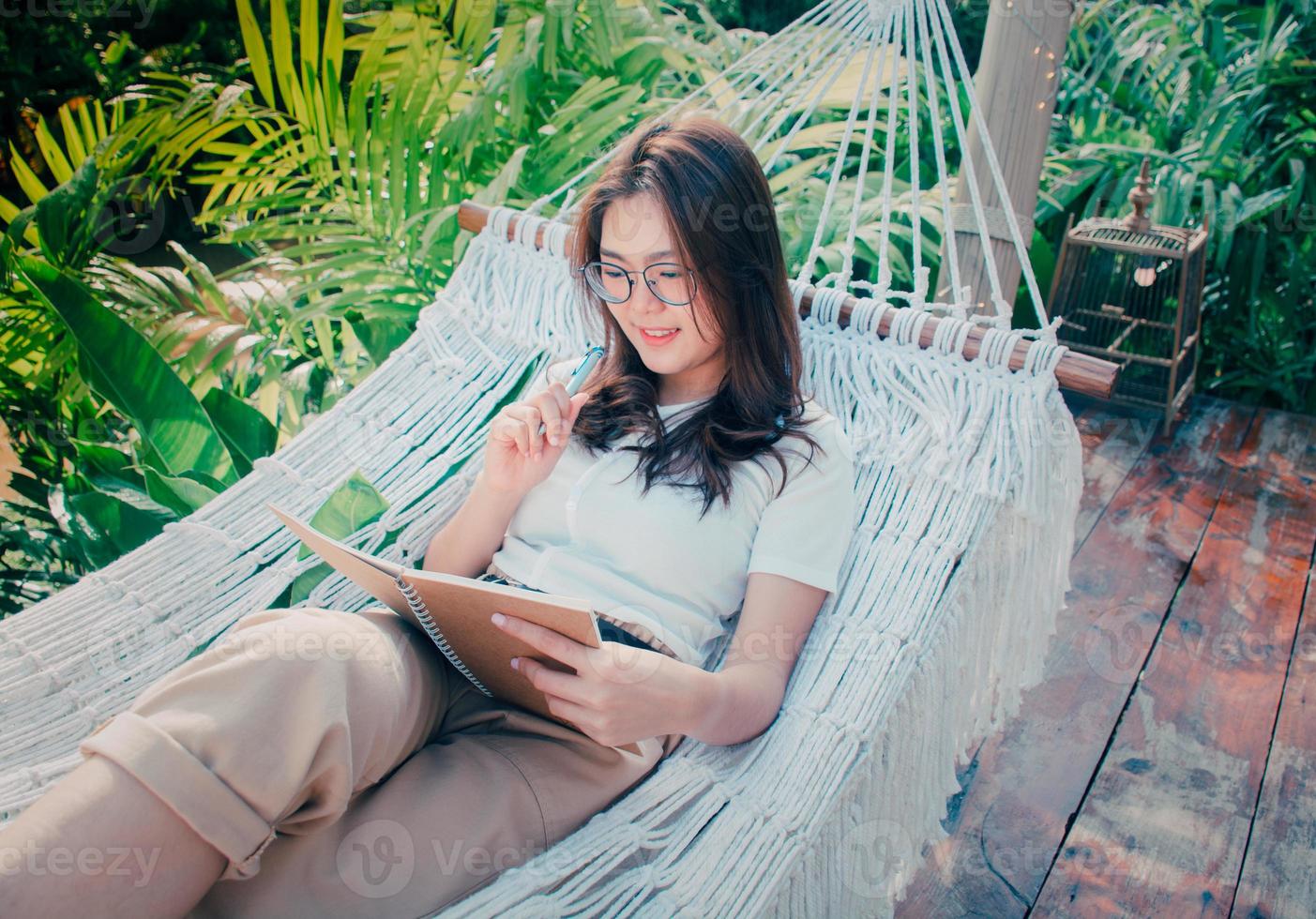 Beautiful Asian Woman Wearing Glasses Taking Note On White Hammock In