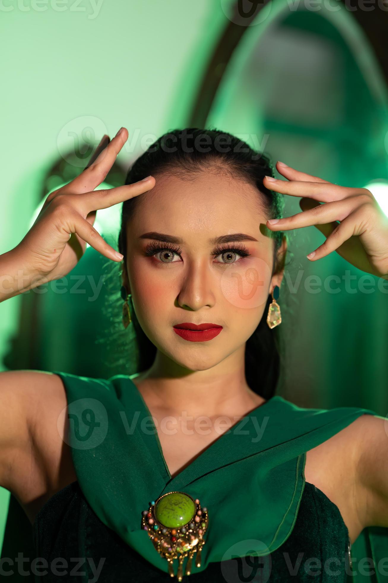 the face with beautiful makeup and red lips of an Asian woman in a green dress and jewelry ...