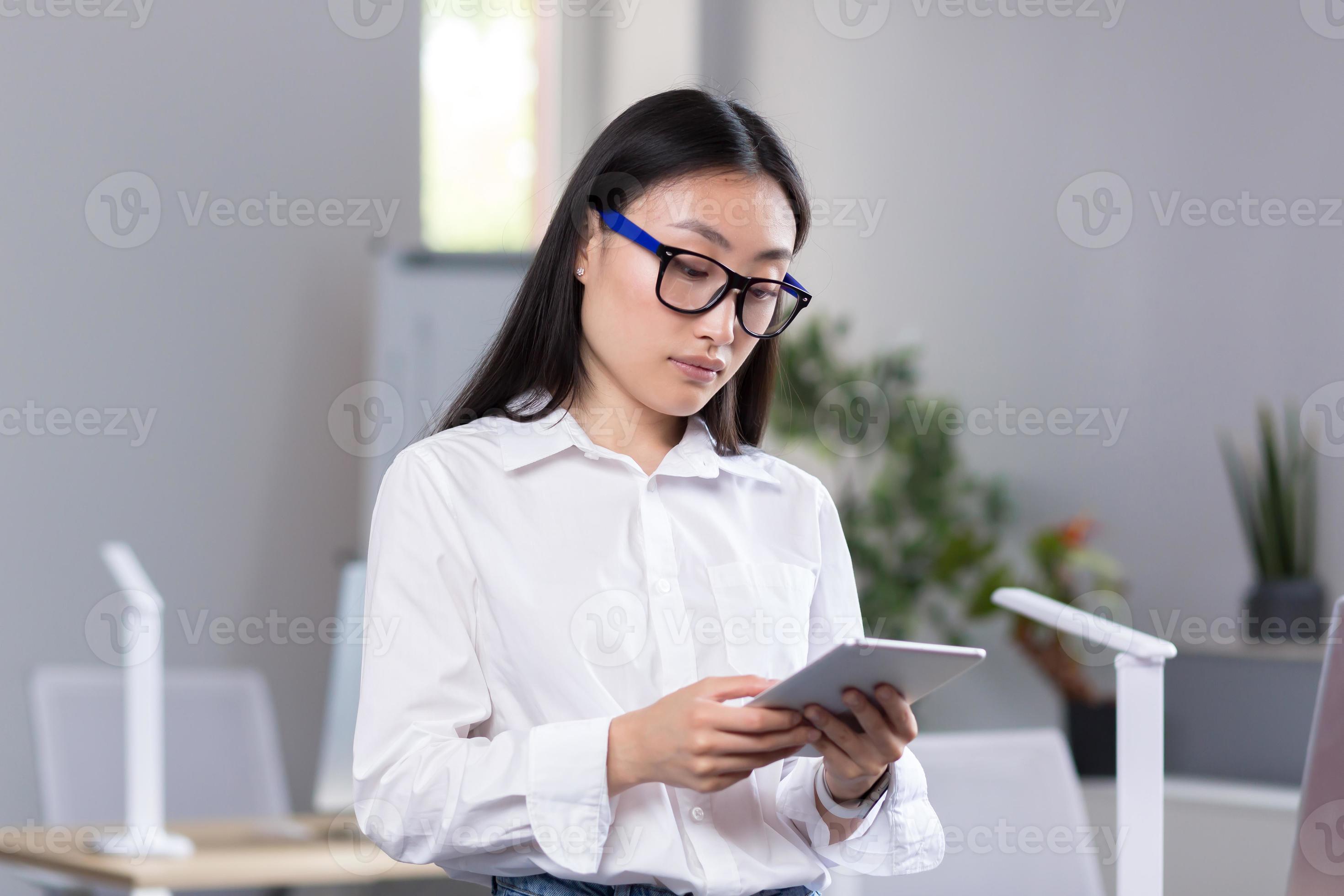 Asian female student . Standing in the office, holding a tablet in his ...