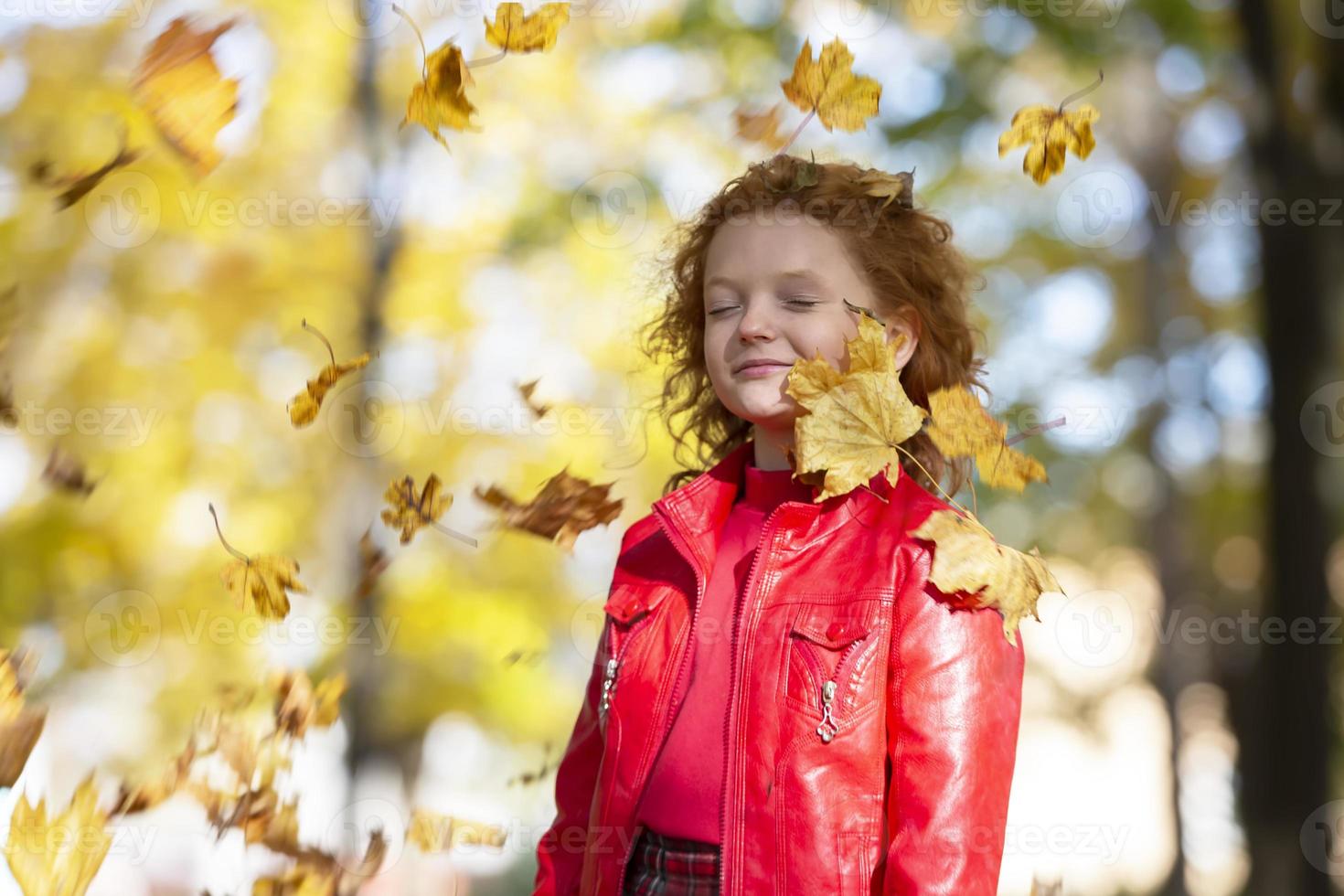 Little red-haired girl against the background of flying autumn leaves ...
