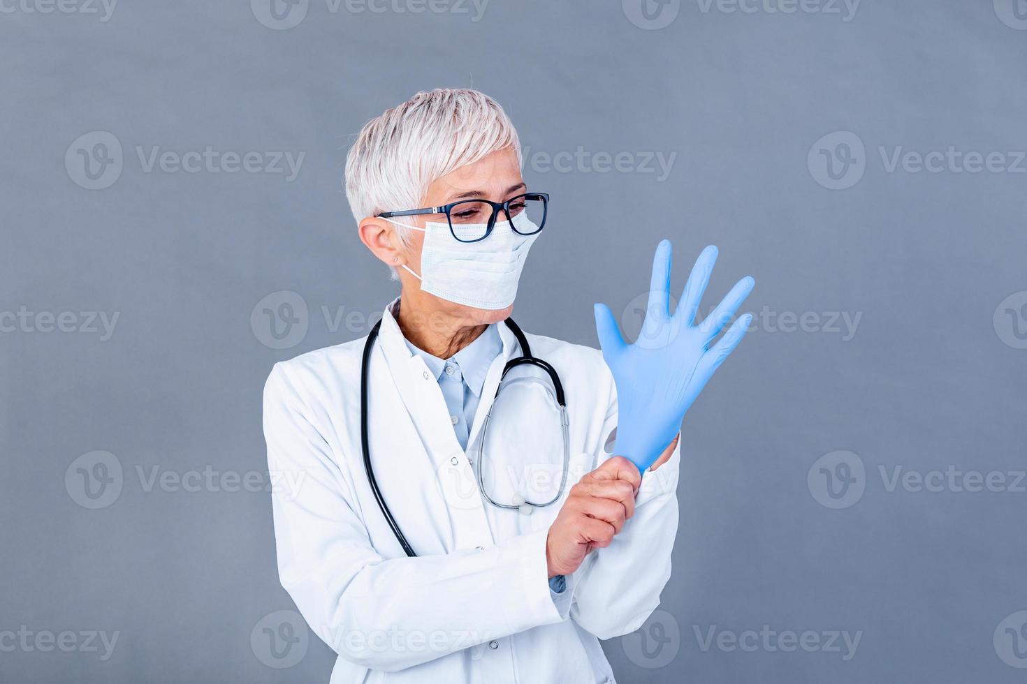 Mature Female Doctor Putting On Protective Gloves And Medical