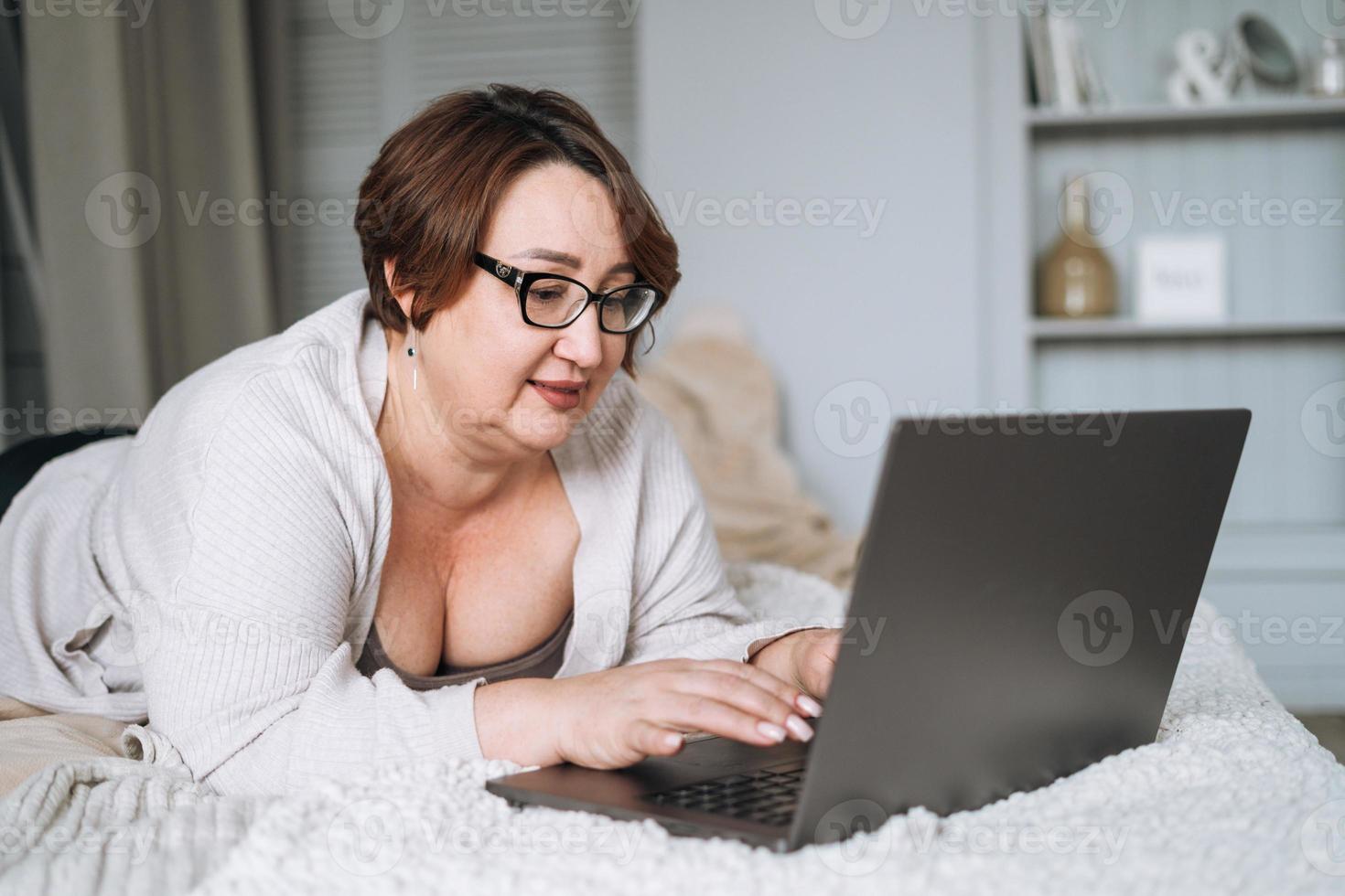 Smiling middle aged plus size woman lying on bed, working on laptop from home 21033279 Stock ...