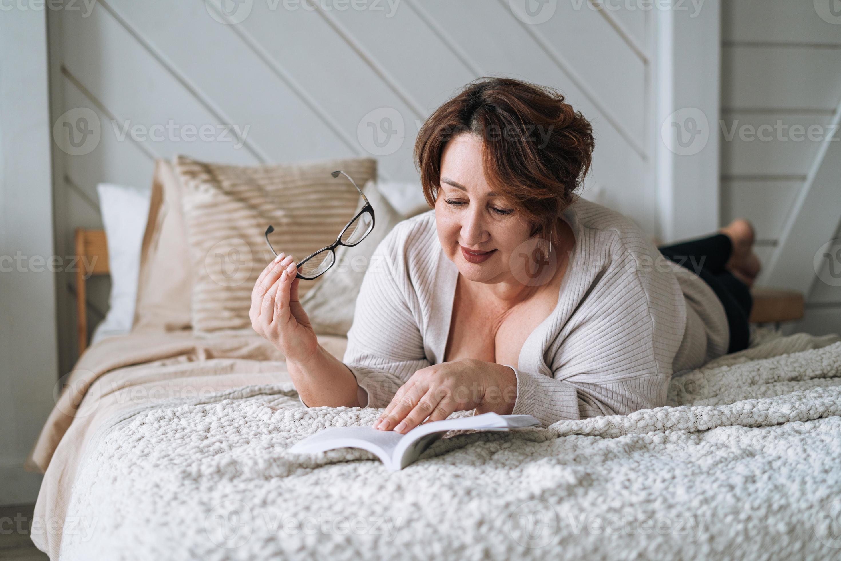 Smiling middle aged plus size woman lying on bed and reading book at home 21033282 Stock Photo ...