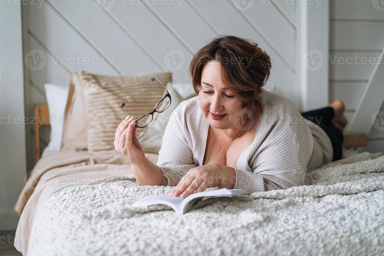 Smiling middle aged plus size woman lying on bed and reading book at home 21033282 Stock Photo ...