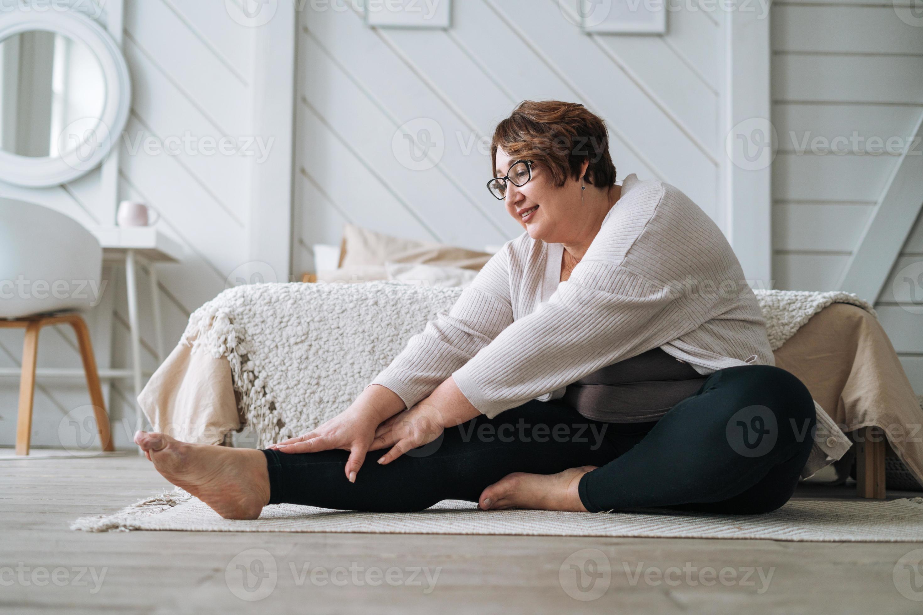 Middle aged plus size smiling brunette woman in home wear doing stretching in bedroom 21033284 ...