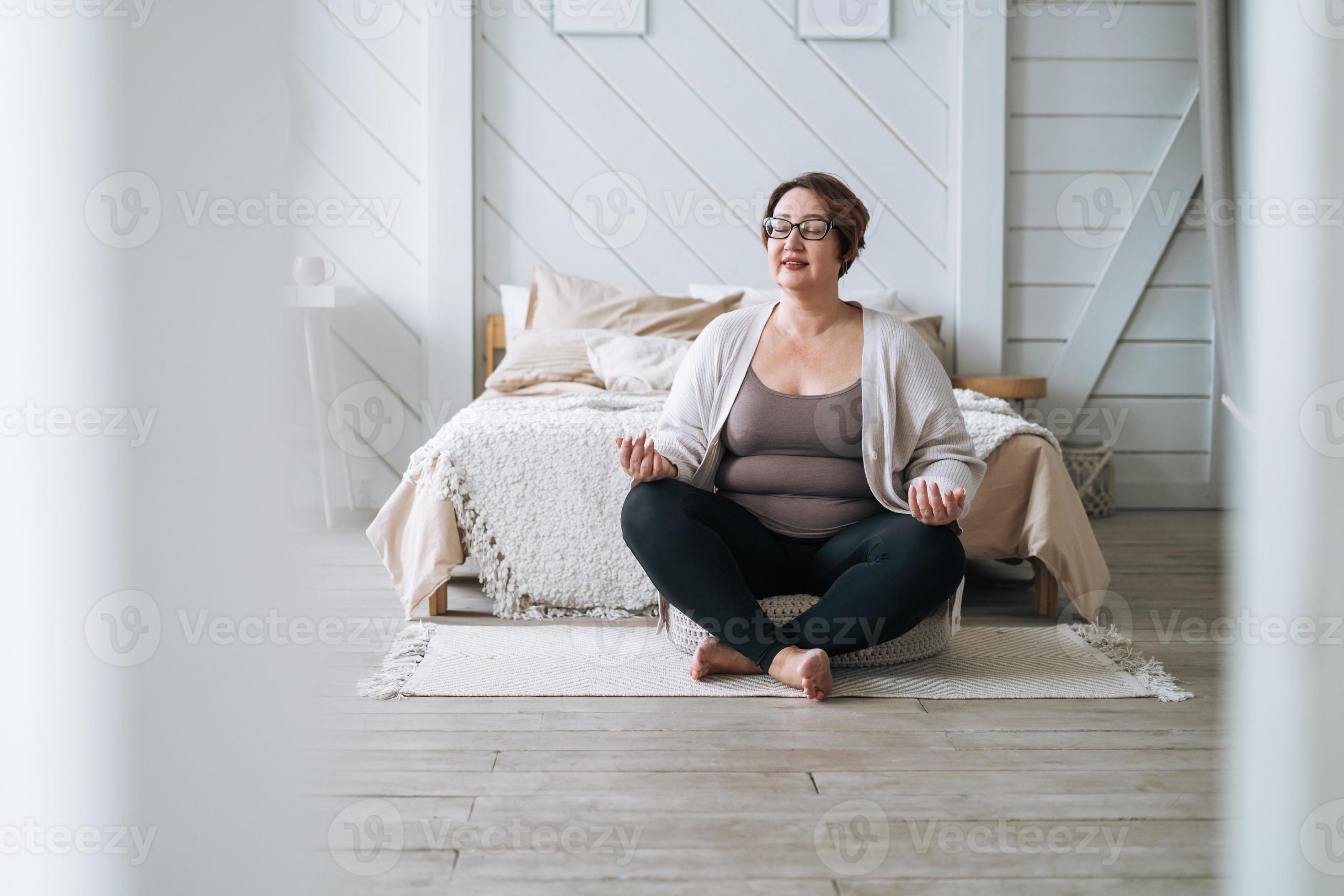 Middle aged plus size smiling brunette woman in home wear practicing yoga in bedroom 21033293 ...