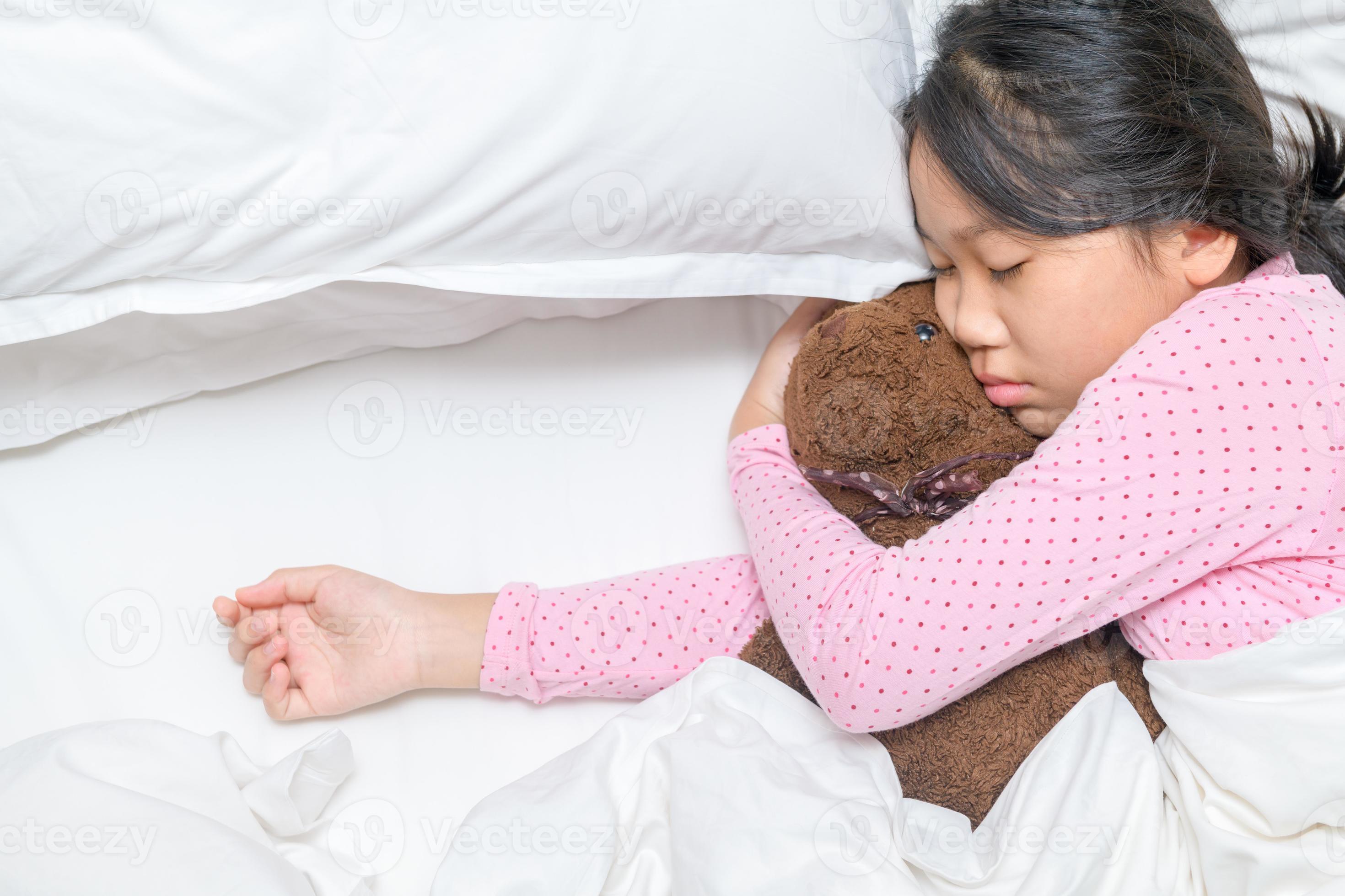 Sweet little girl is hugging a teddy bear while sleeping in her bed at ...