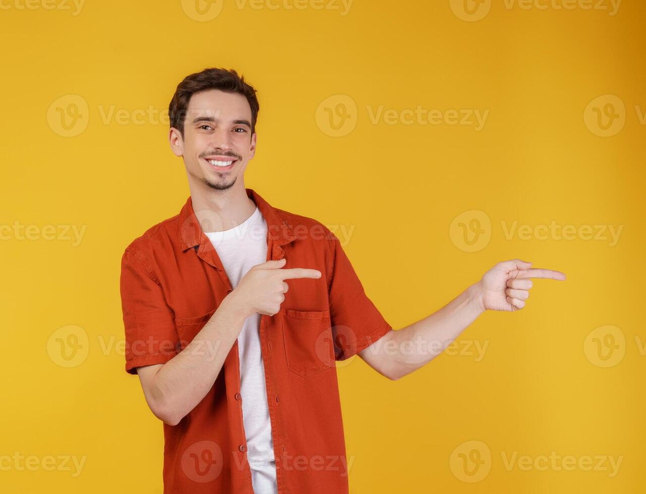 Portrait of young man pointing fingers at copy space isolated on yellow ...
