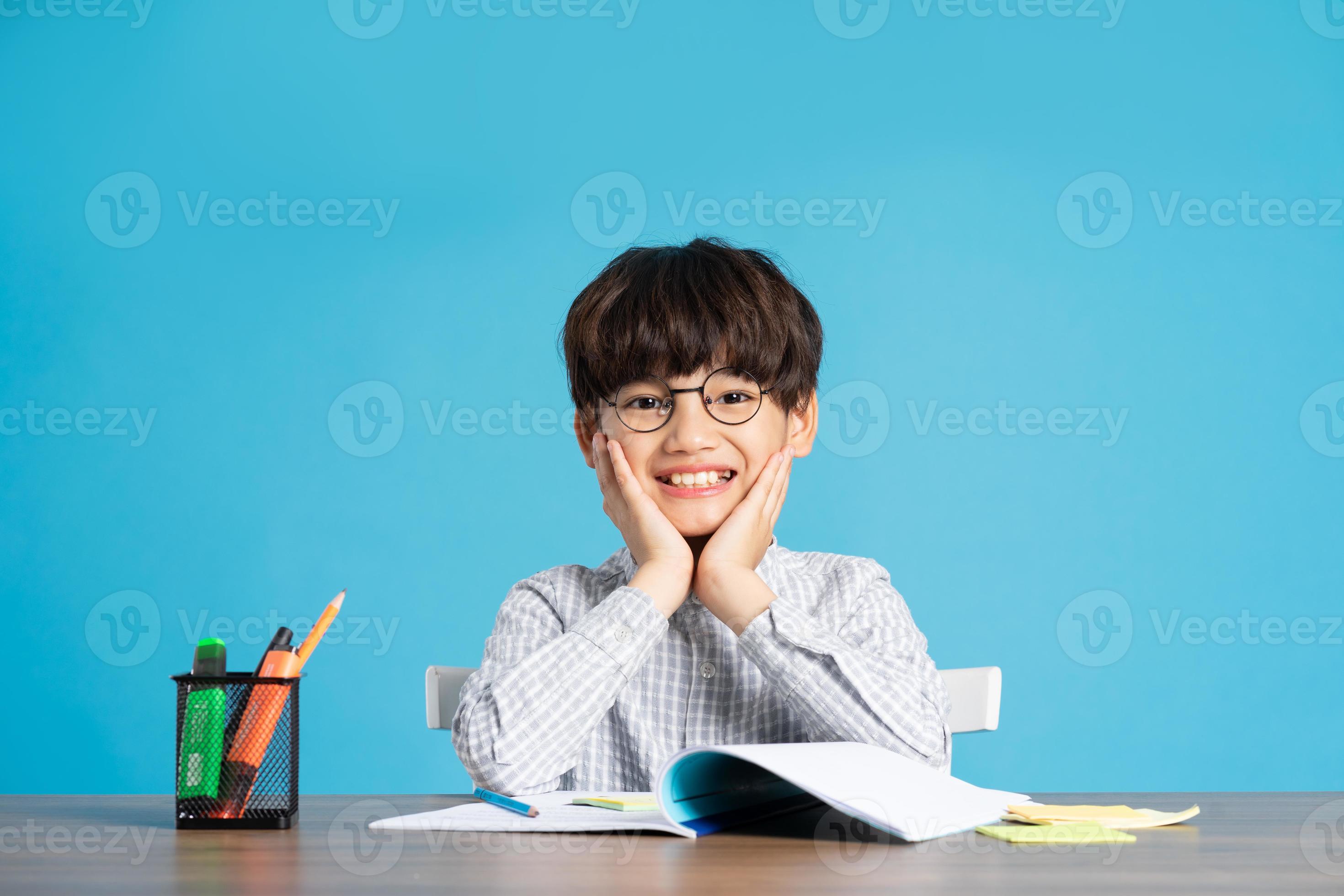 portrait of school boy sitting and studying on a blue background ...