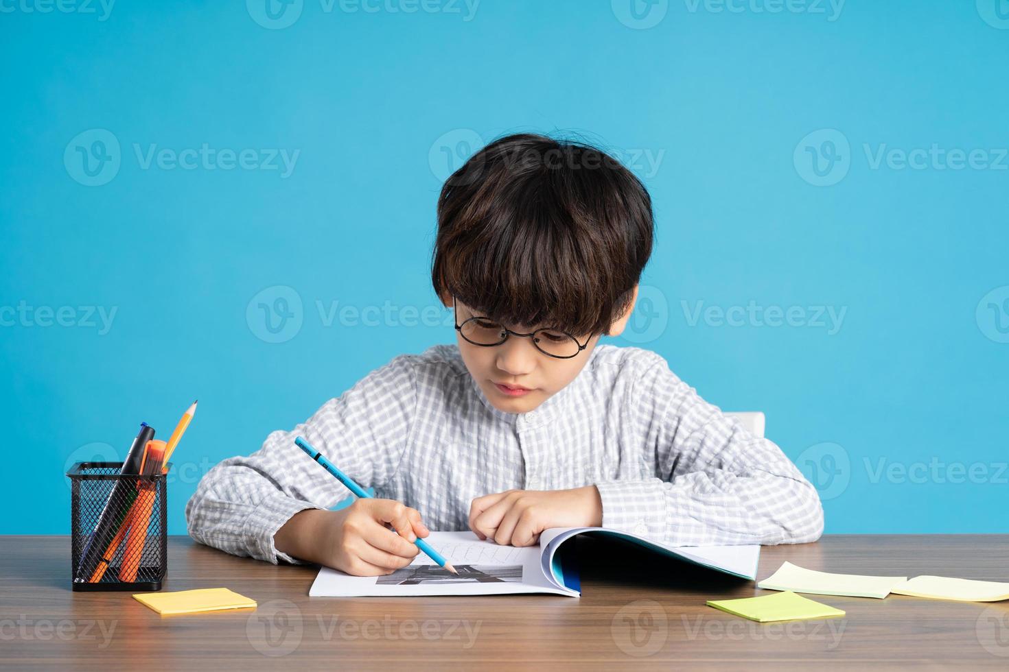 portrait of school boy sitting and studying on a blue background ...