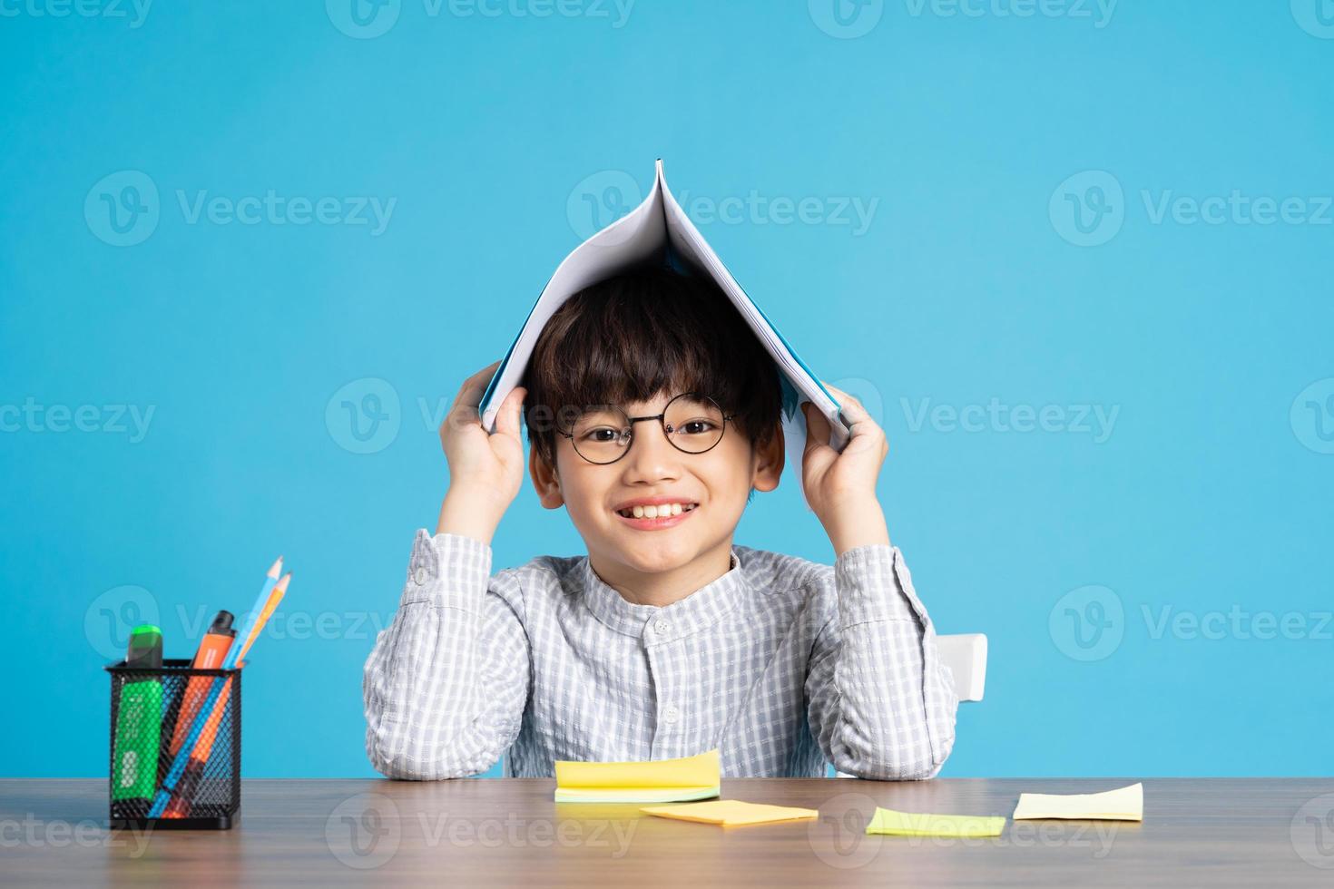 portrait of school boy sitting and studying on a blue background ...
