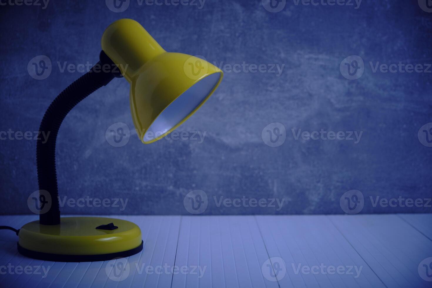 Bright yellow desk lamp, turned off, standing in dark against background concrete wall. 22024564 ...