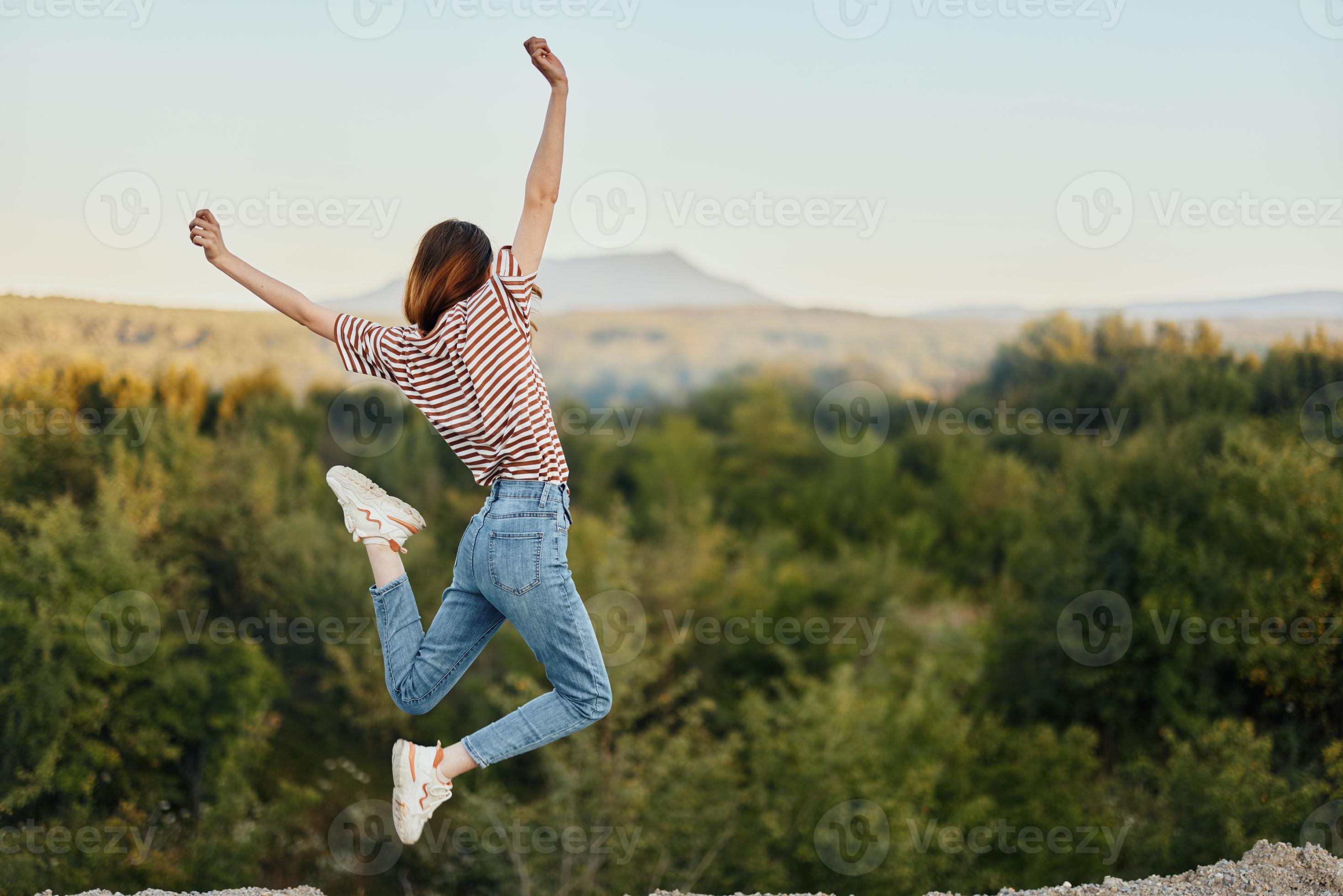 Happy woman jumping up from happiness in nature with her back to the camera with a beautiful ...