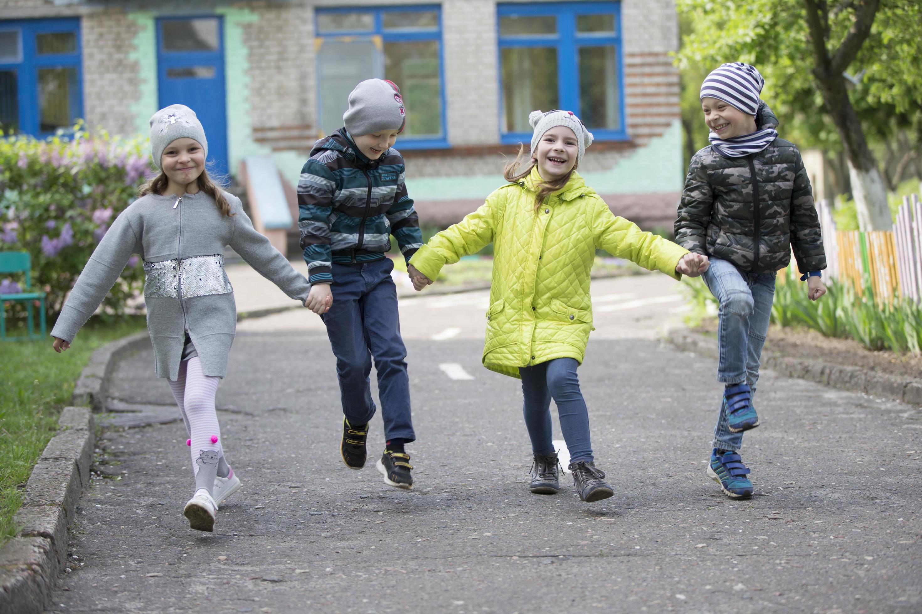 Happy preschoolers on the street. Children holding hands jumping. A ...