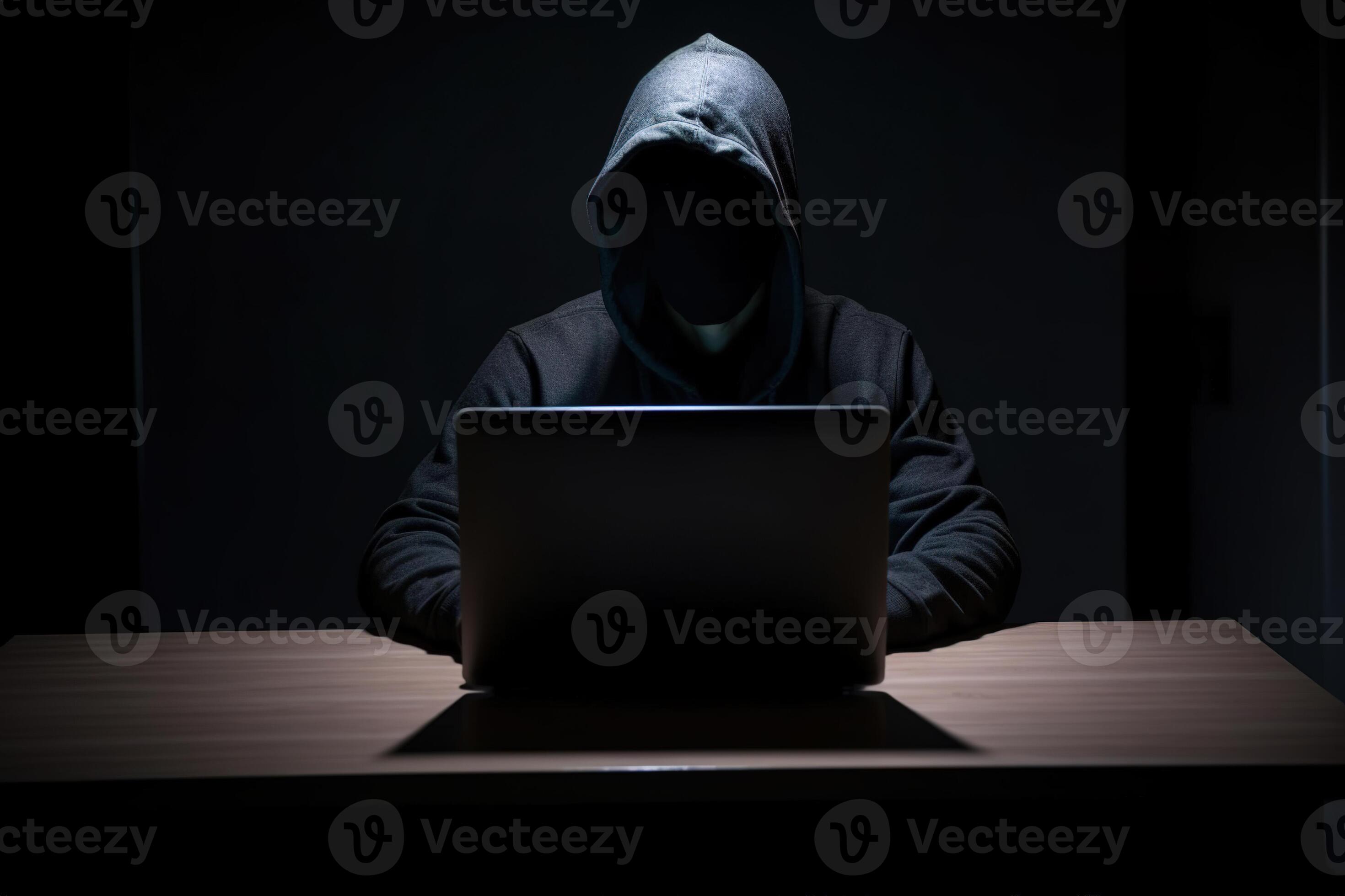 Hacker wearing black hoodie using laptop computer while working on dark background. 22813408 ...