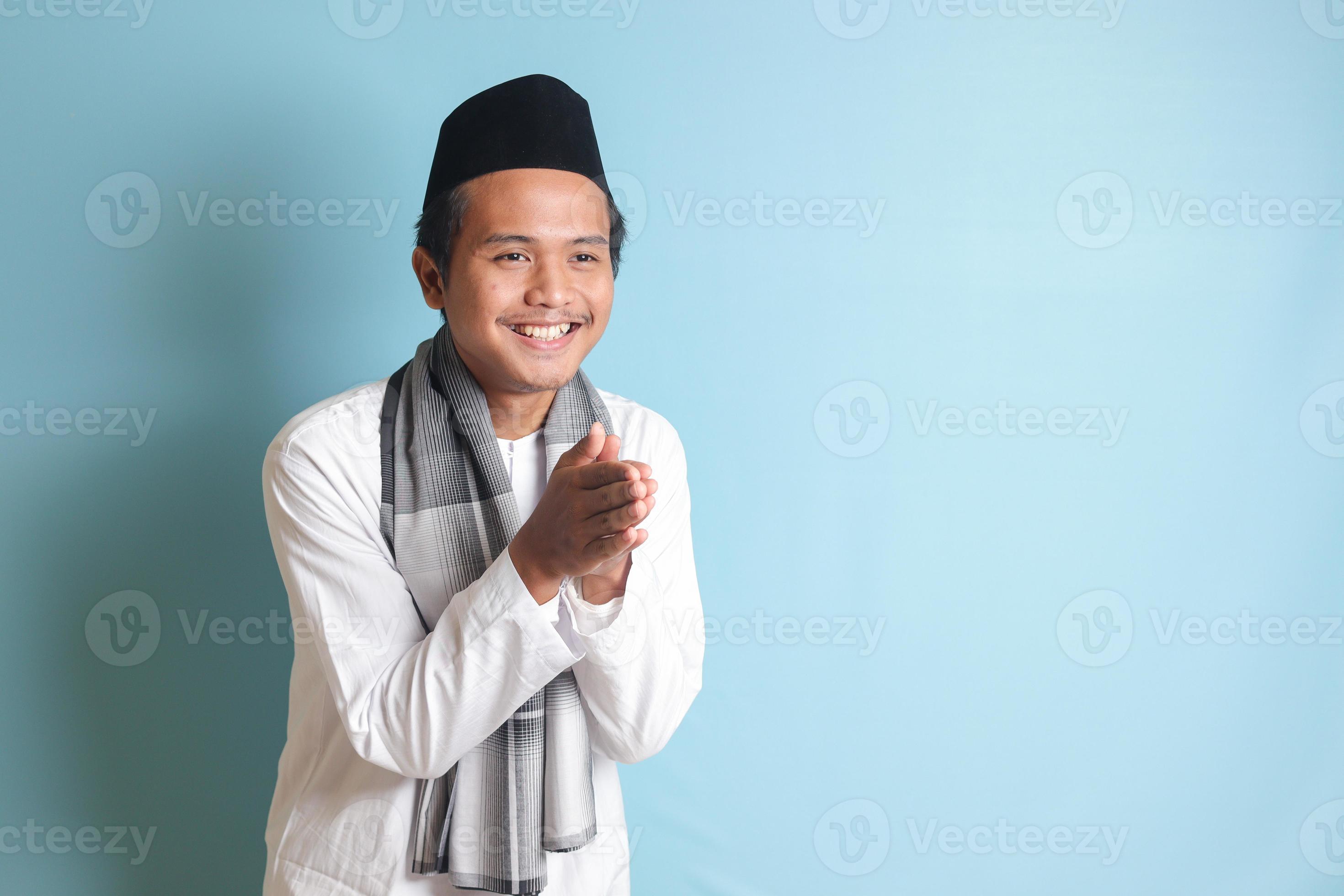 Portrait of Asian muslim man in white koko shirt with skullcap showing apologize and welcome ...
