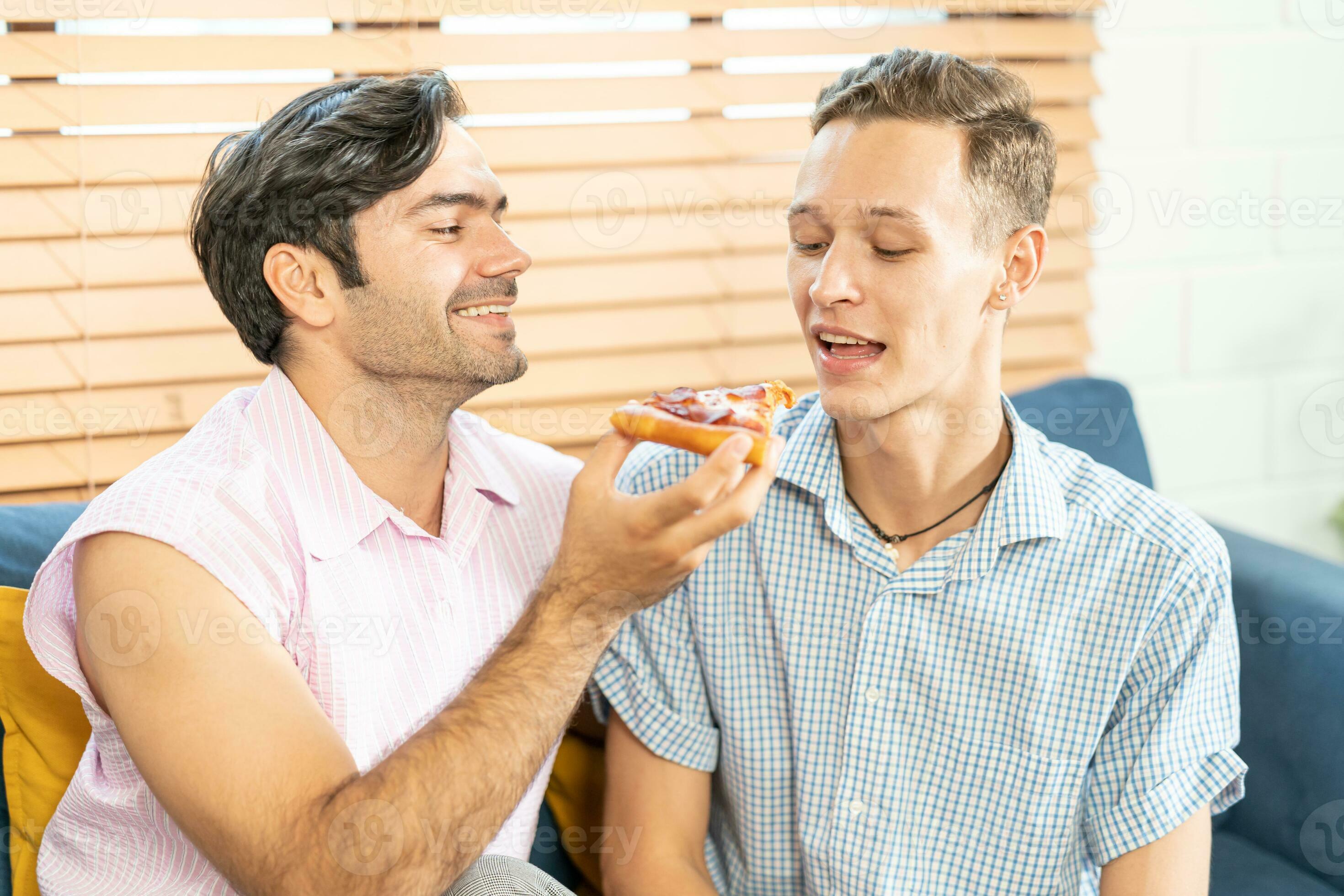 Cheerful Gay Couple Eating Pizza Gay Couple Sitting On Sofa At Home Eating One Slice Of Pizza