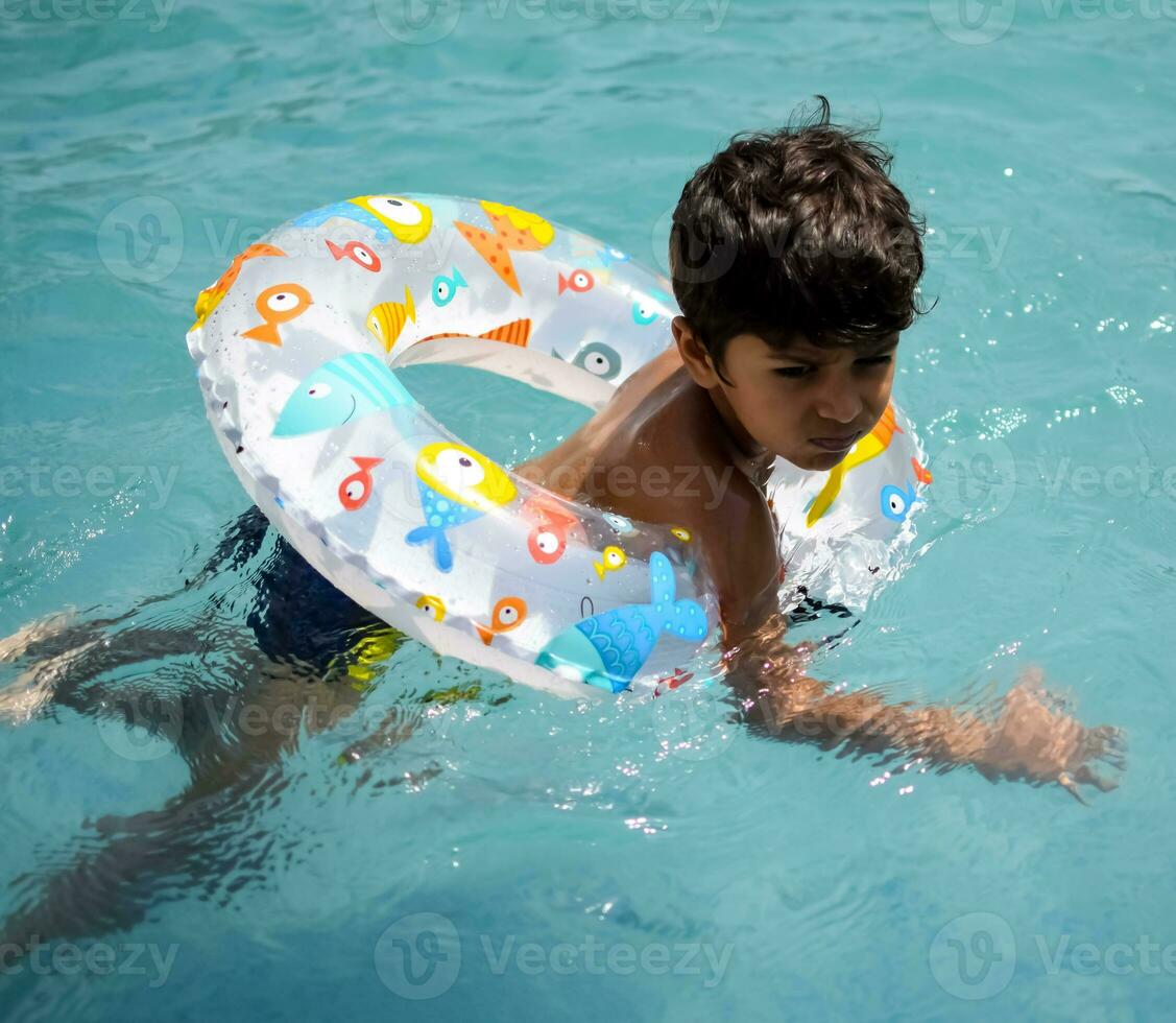 Happy Indian boy swimming in a pool, Kid wearing swimming costume along with air tube during hot ...
