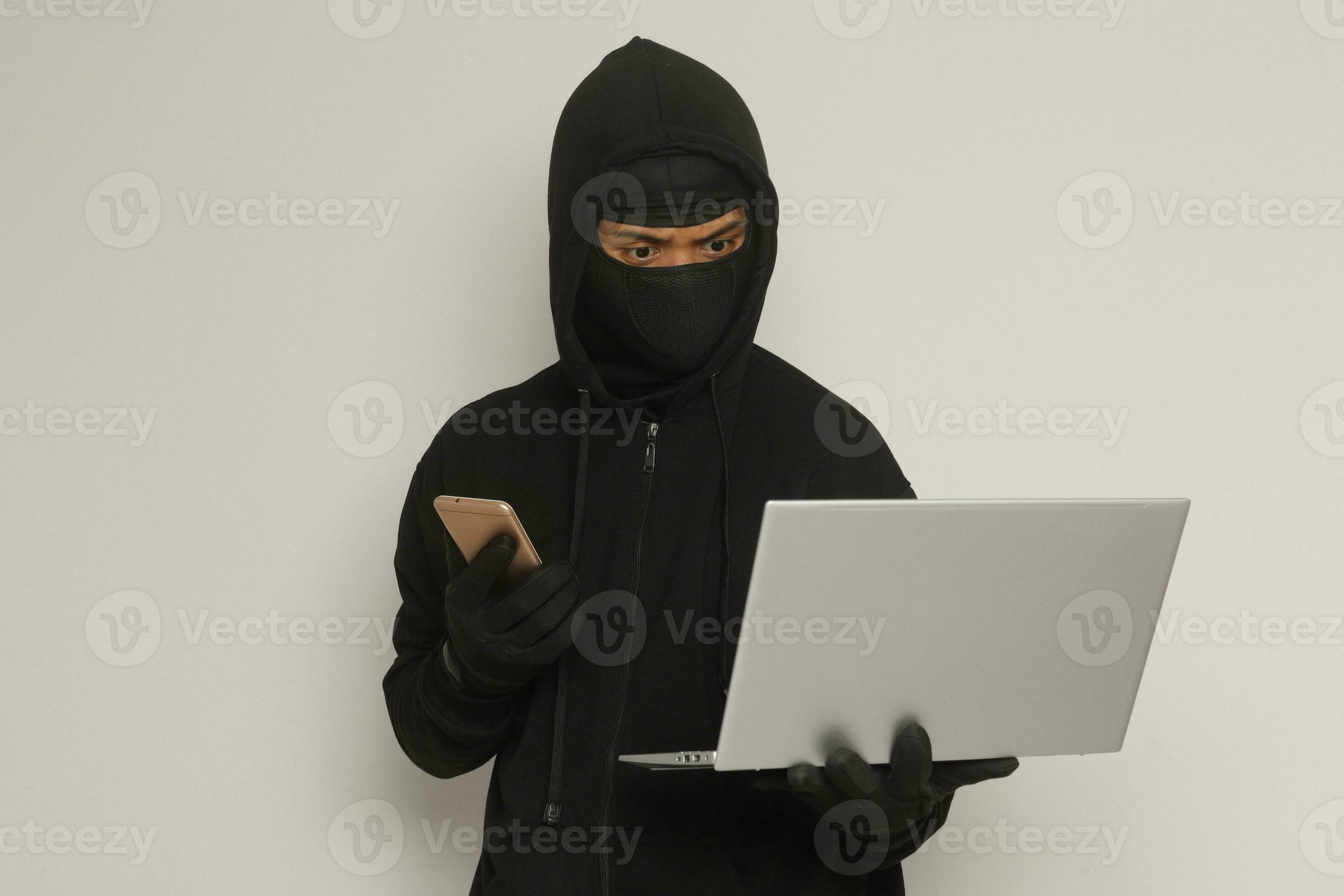 Portrait of mysterious man wearing black hoodie and mask doing hacking ...