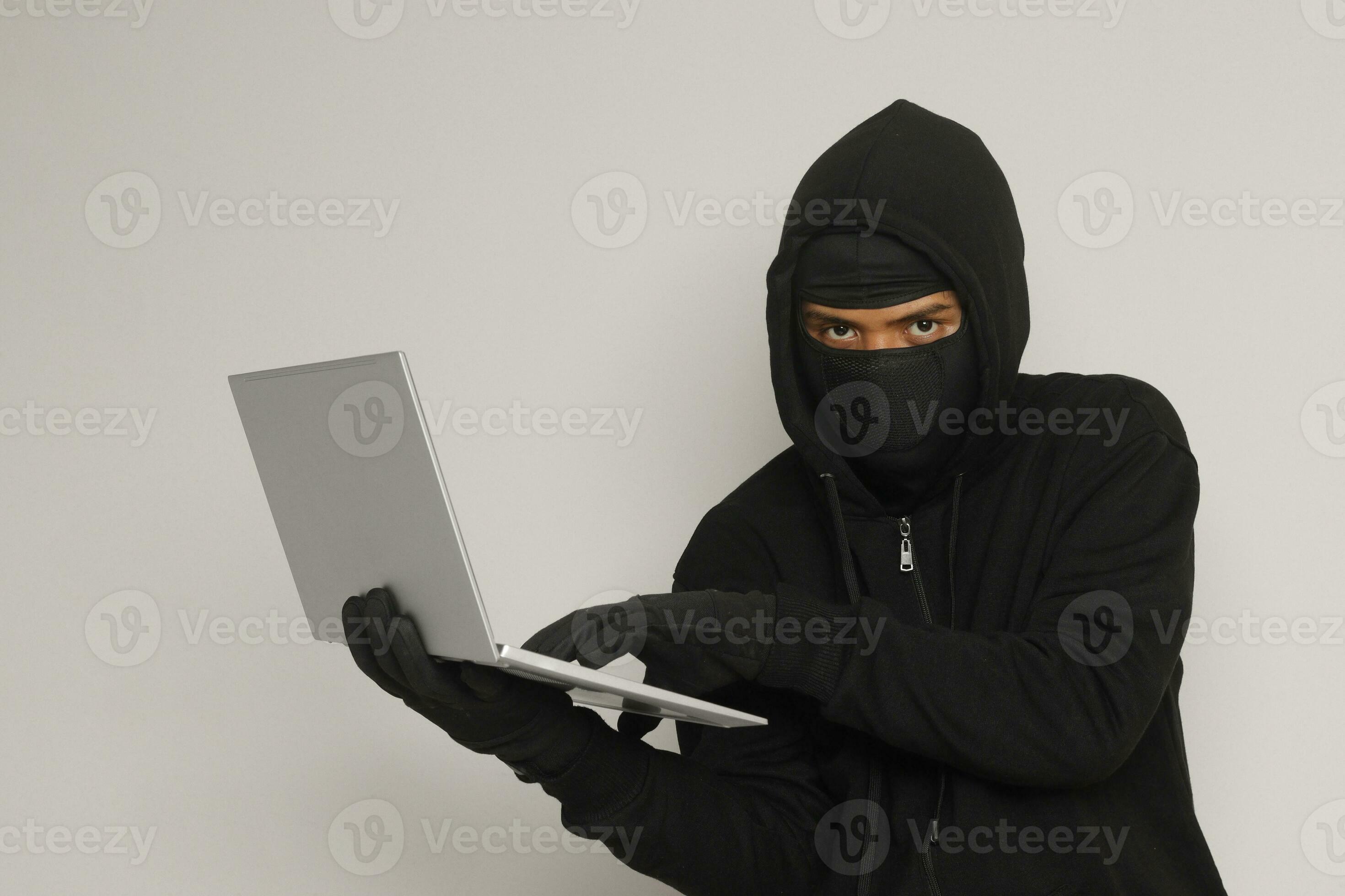 Portrait of mysterious man wearing black hoodie and mask doing hacking ...