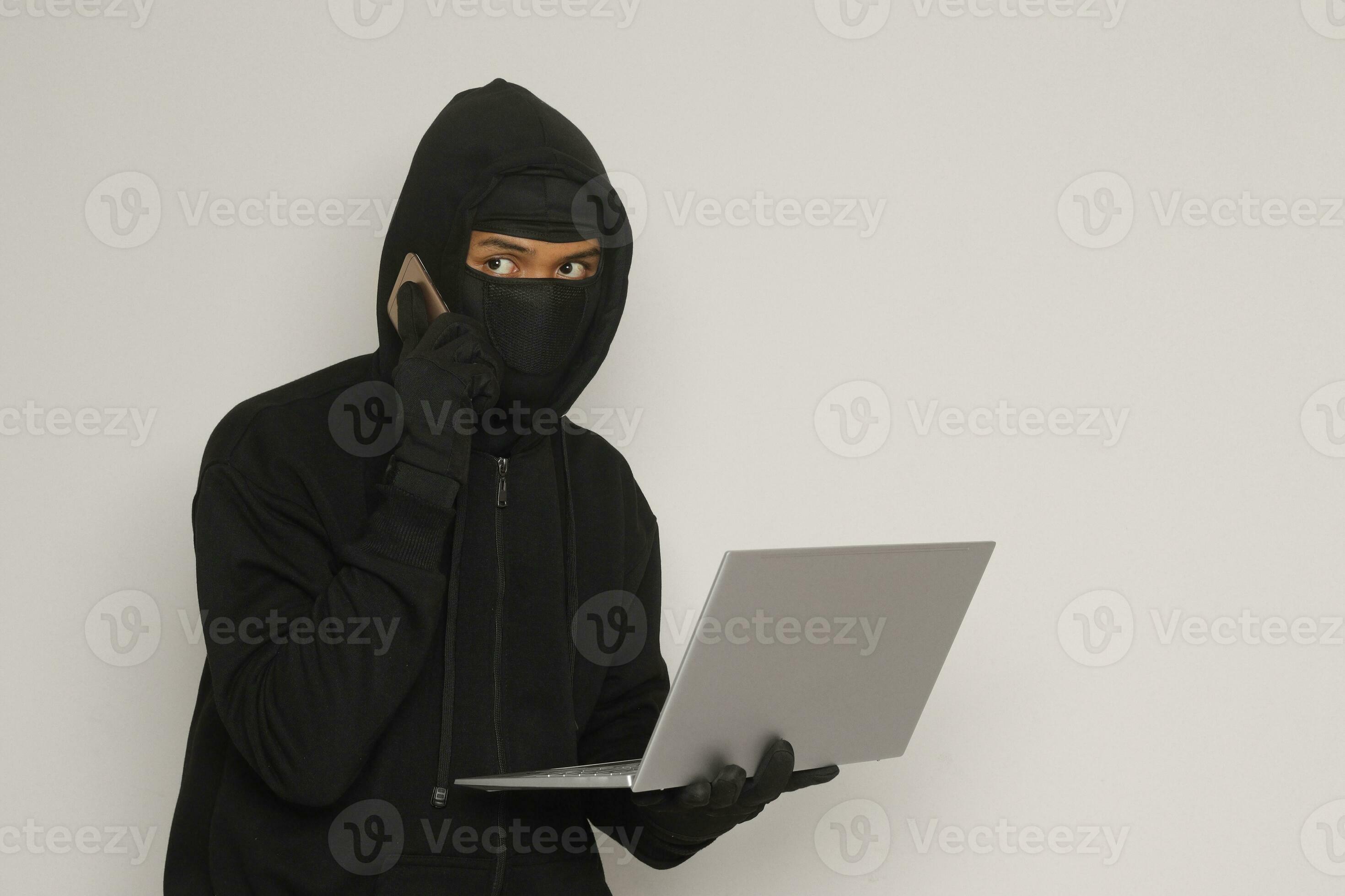 Portrait of mysterious man wearing black hoodie and mask doing hacking ...