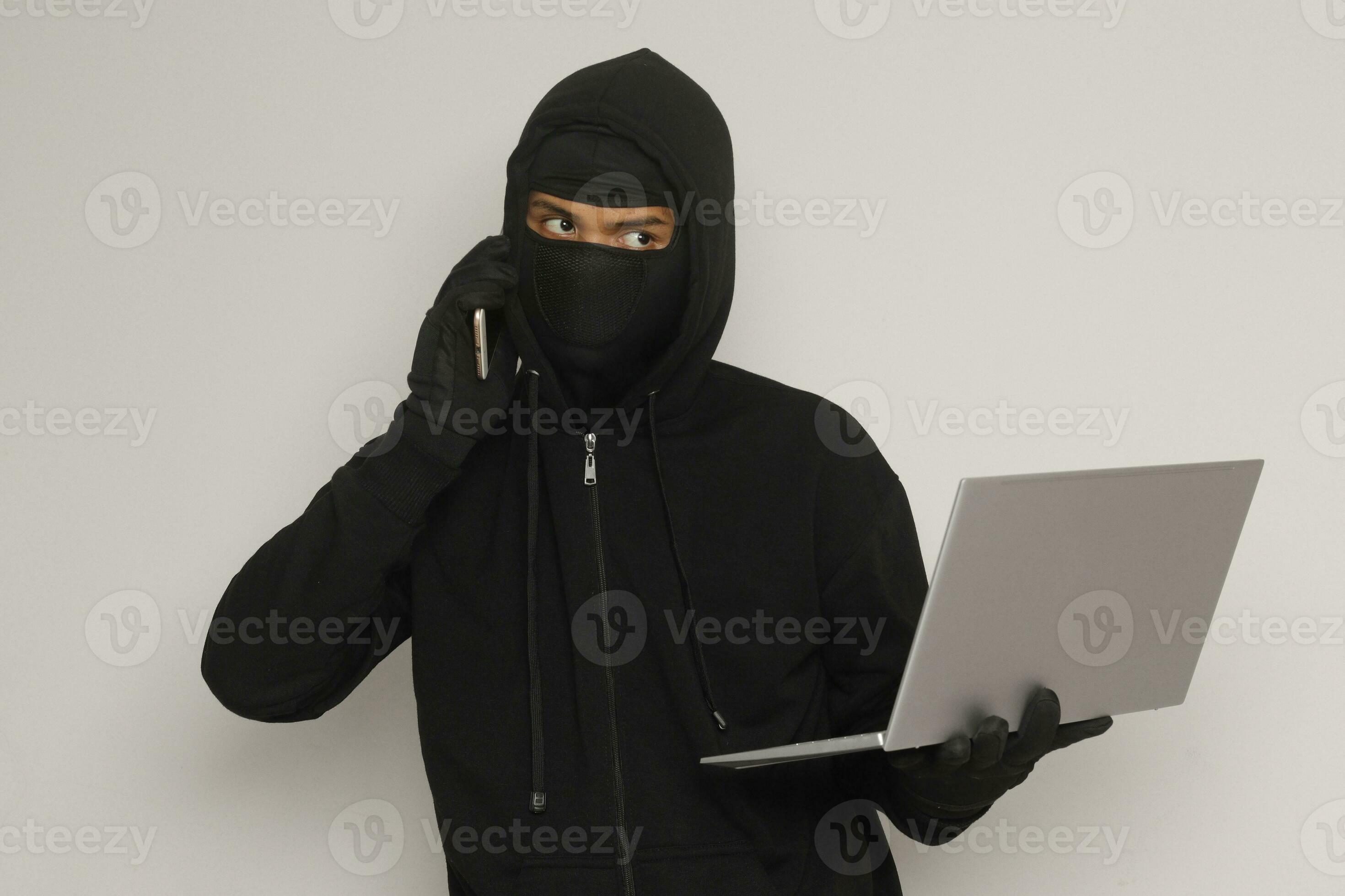 Portrait of mysterious man wearing black hoodie and mask doing hacking ...