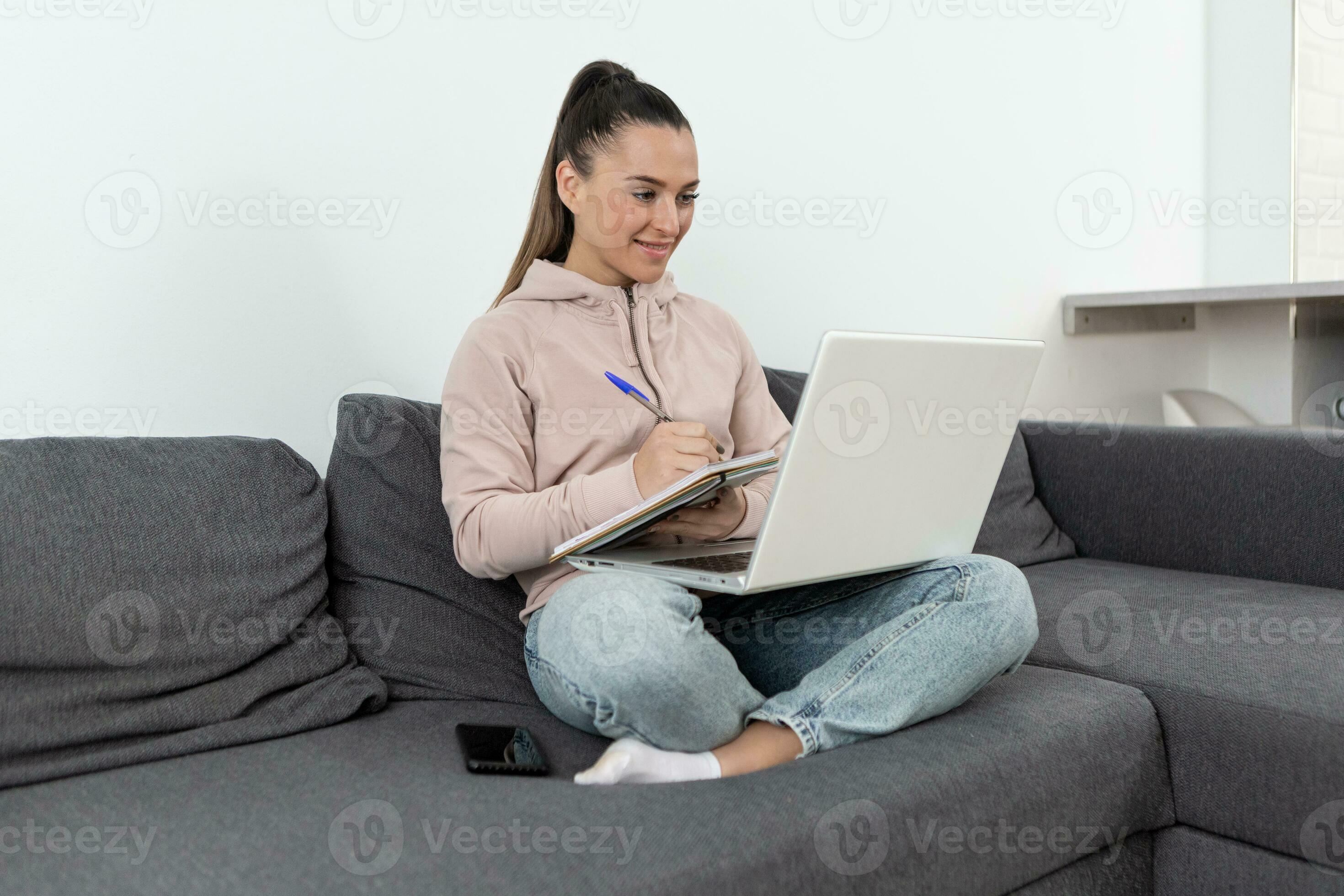 Smiling woman sitting on the sofa at home writing in a notebook while ...