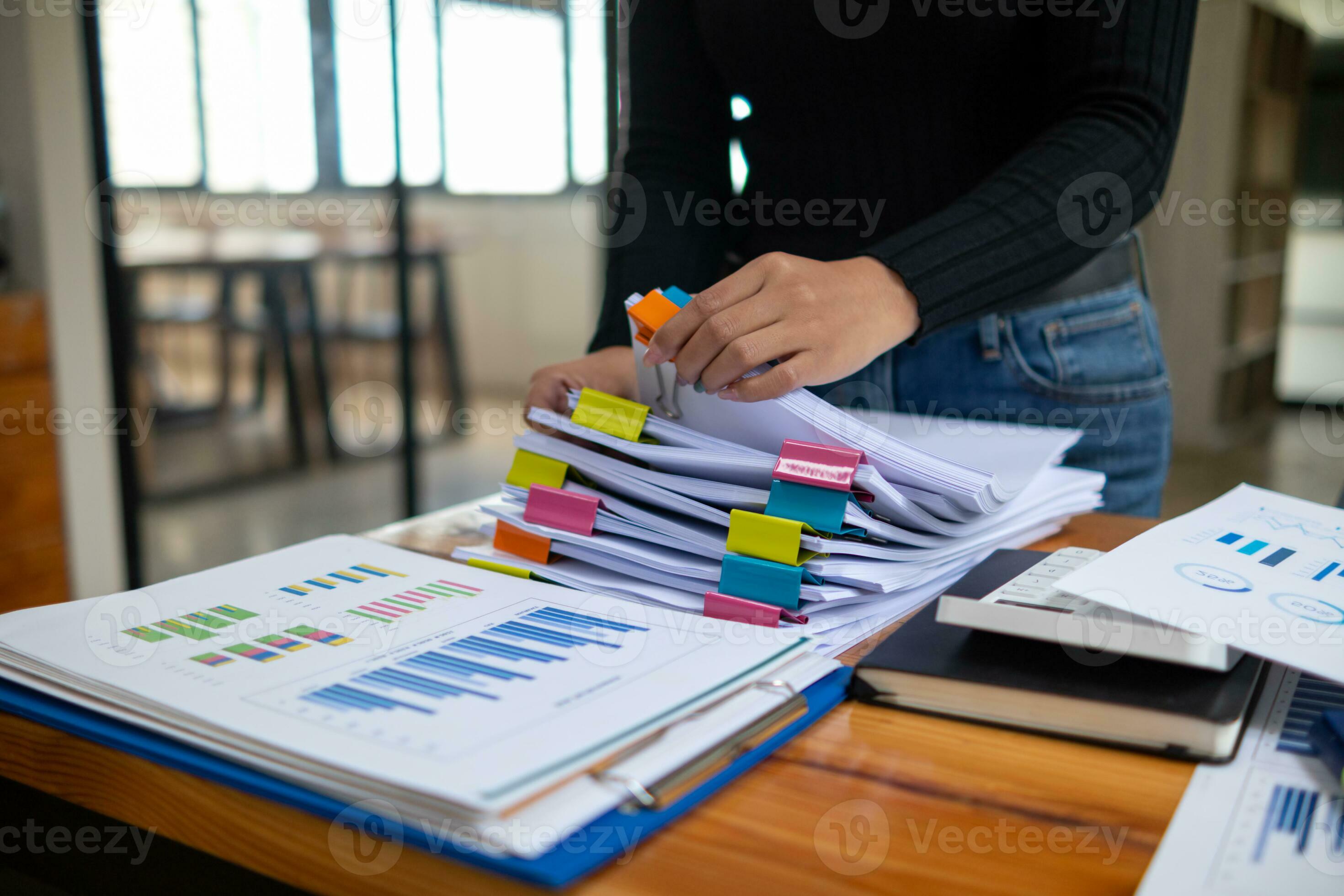 Businesswoman hands working on stacks of paper documents to search and review documents piled on ...