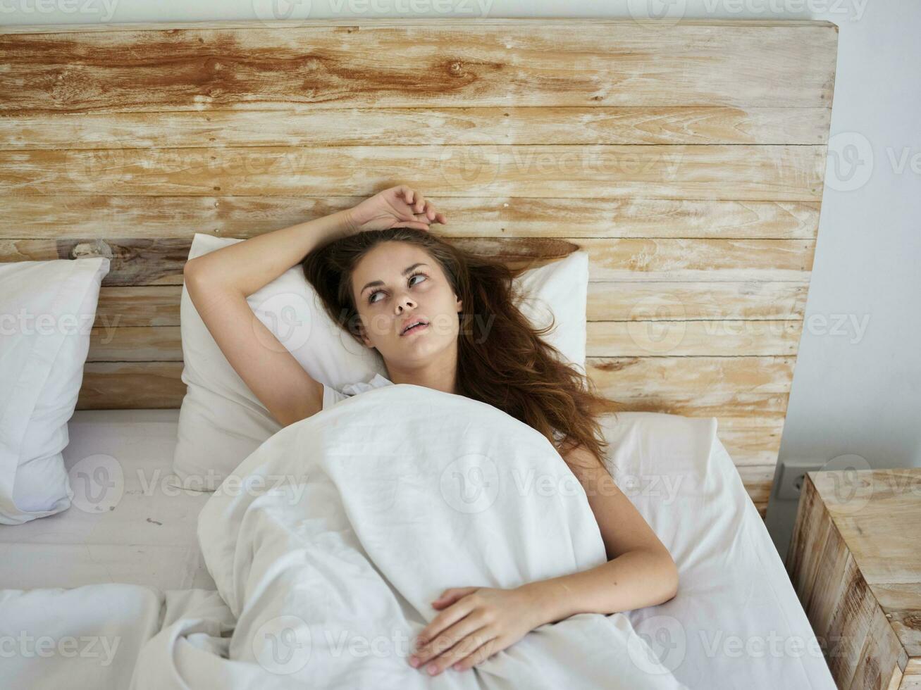 A Woman Lies In Bed Under The Covers In The Morning A Look To The Side
