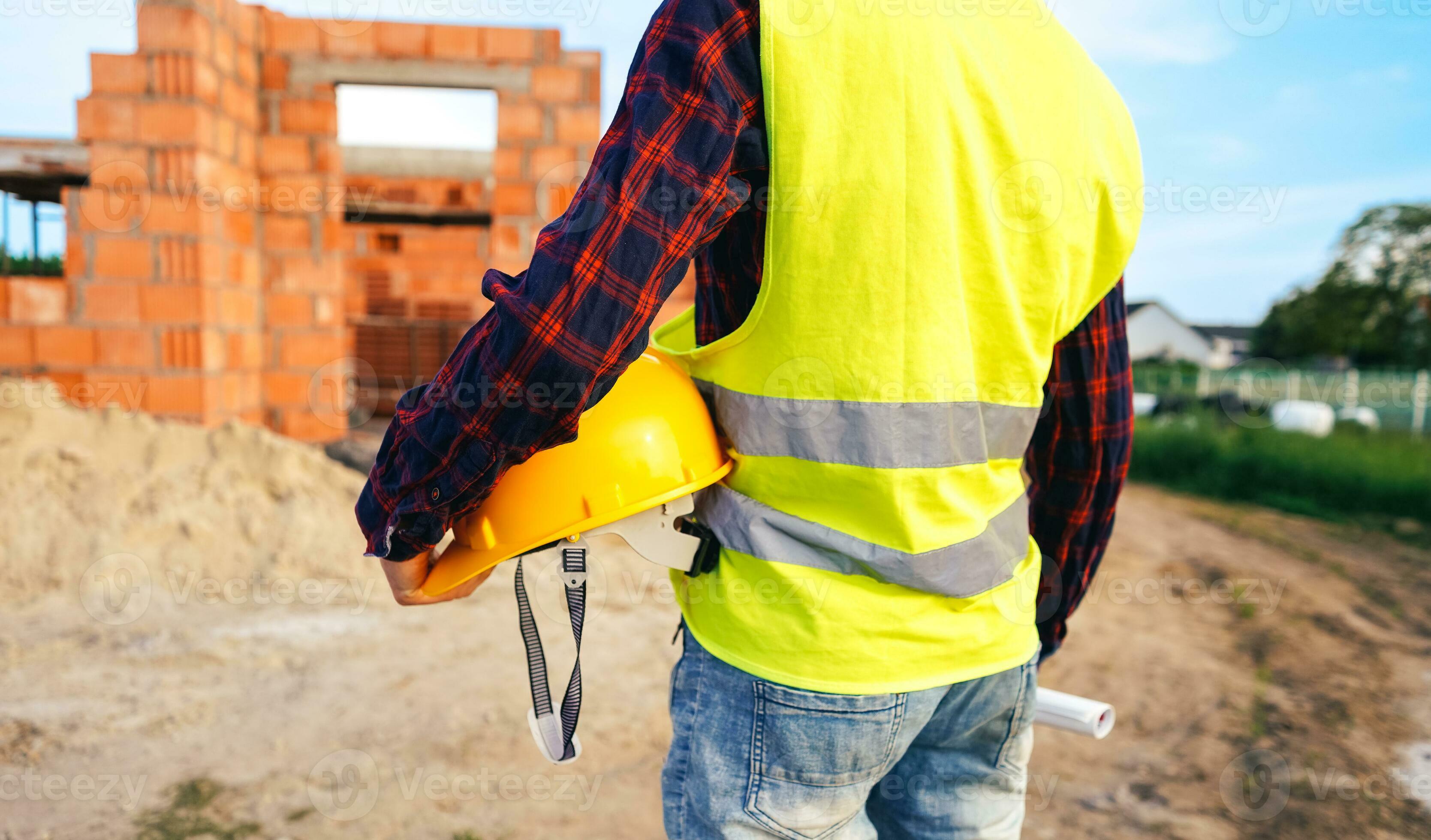 Construction worker on site zone. Worker in yellow vest holding hard ...