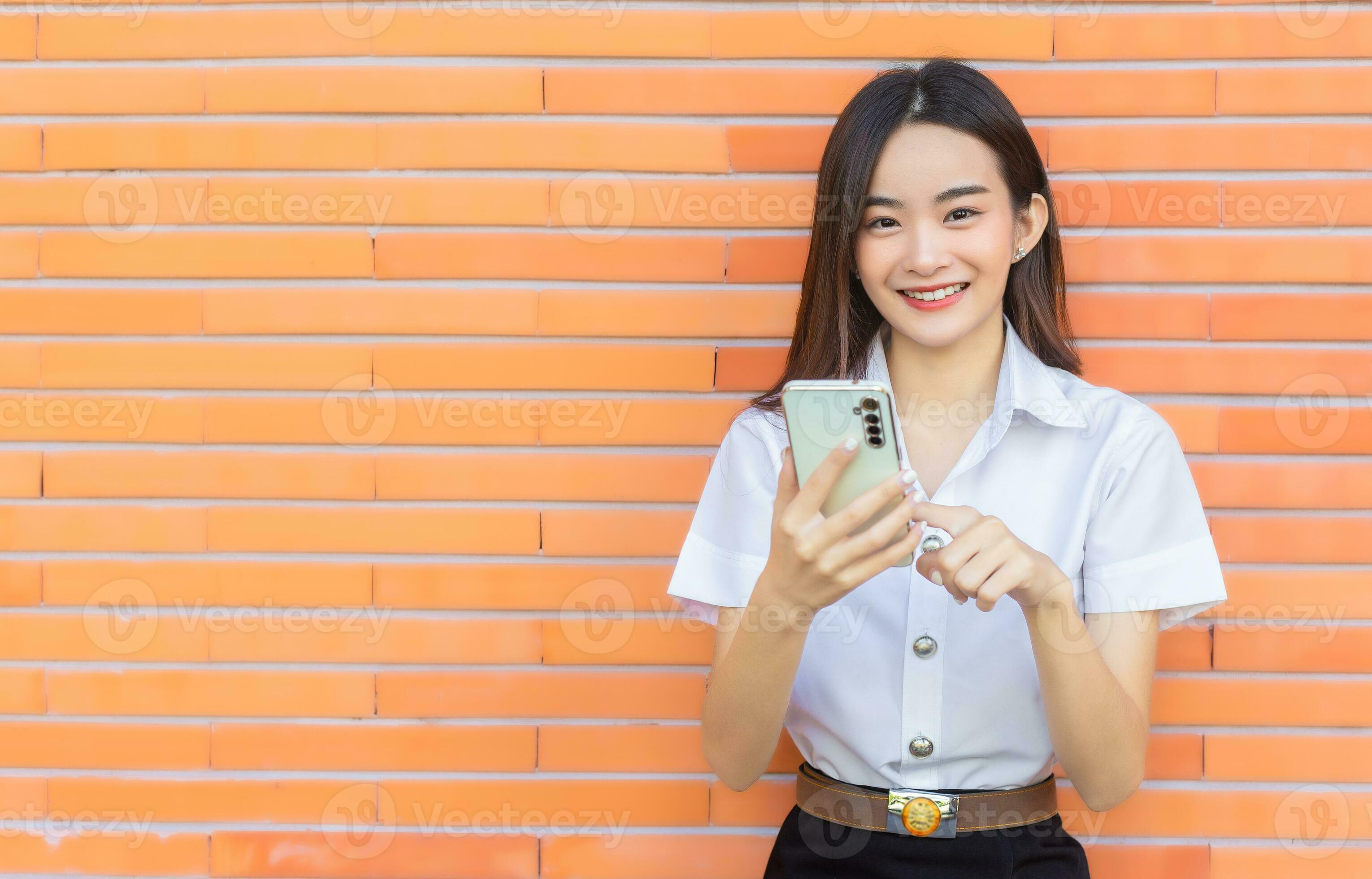 Portrait young Asian beautiful and pretty Thai girl student in uniform while using smartphone ...