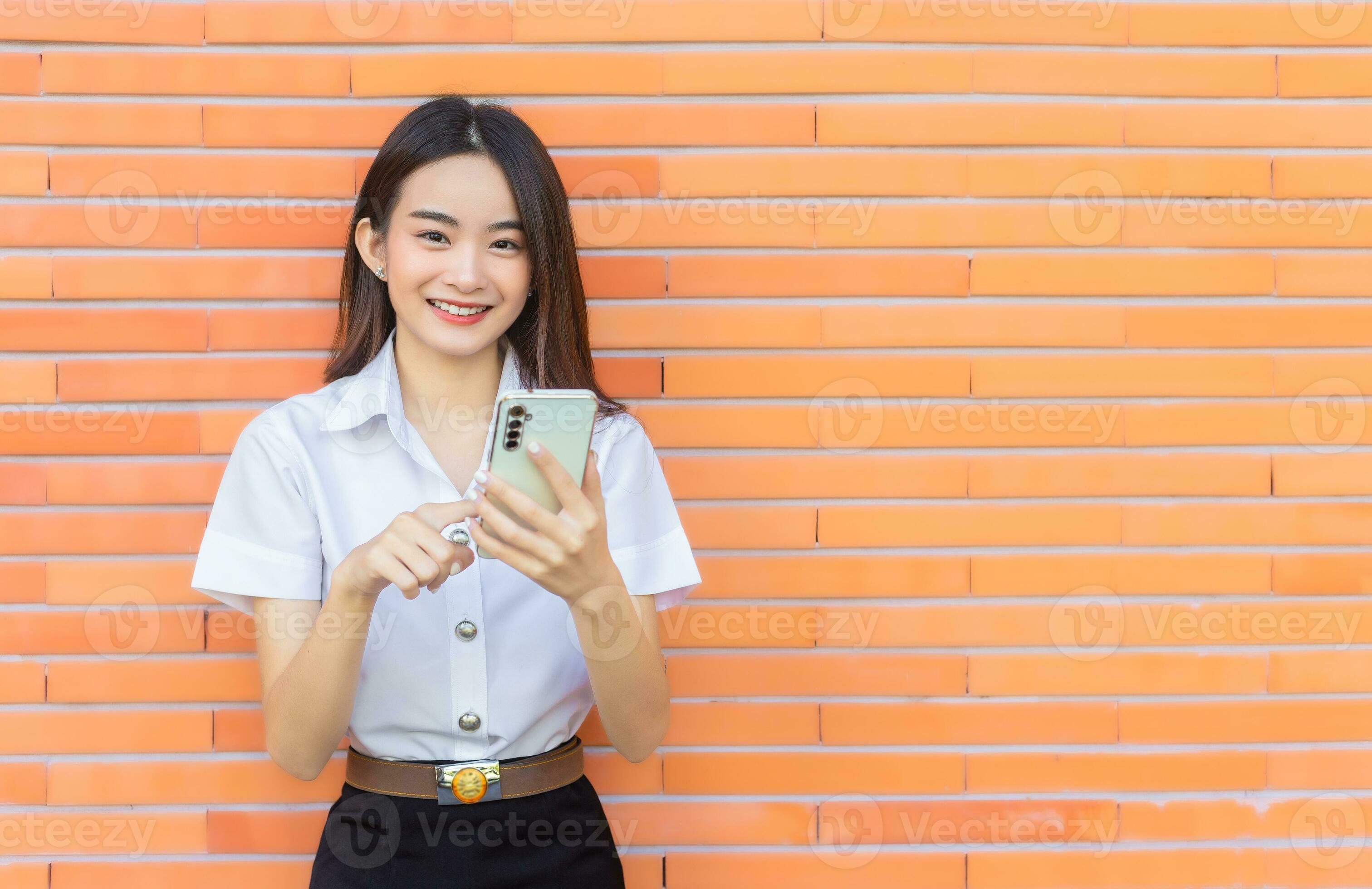 Portrait young Asian beautiful and pretty Thai girl student in uniform while using smartphone ...