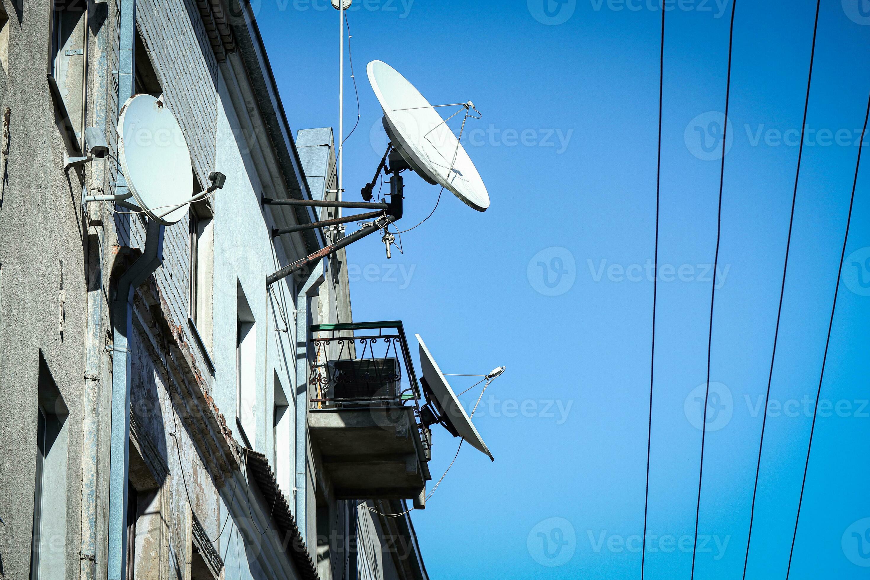 White satellite dish antennas on the roof and wall of ann old building with lines or wires on ...