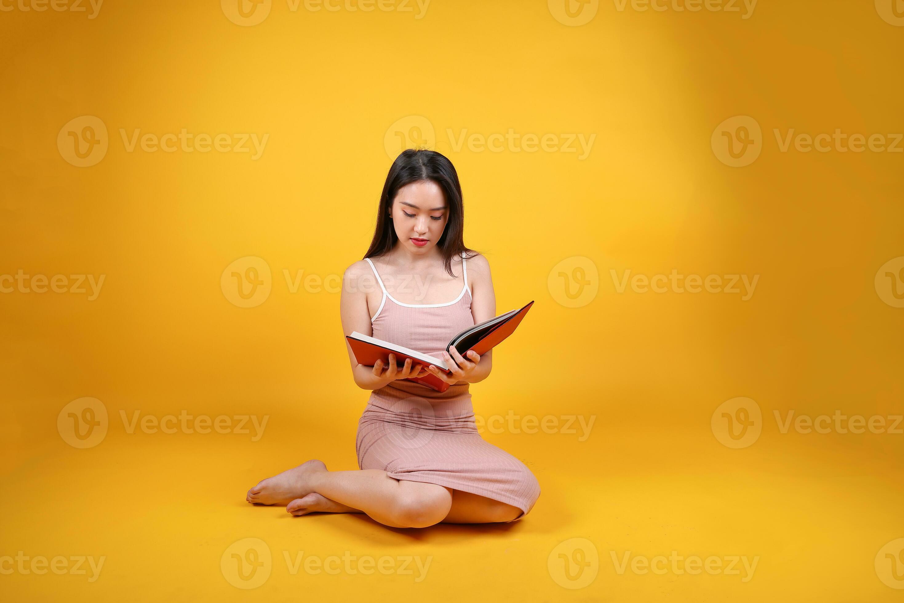 Beautiful young south east Asian woman sit down on floor yellow orange color background read ...