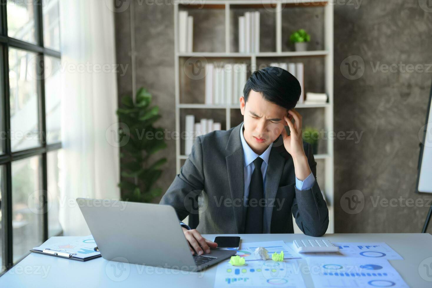 Frustrated young businessman working on a laptop computer sitting at ...