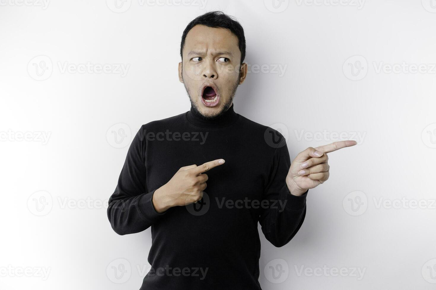 Shocked Asian man wearing black shirt pointing at the copy space beside ...