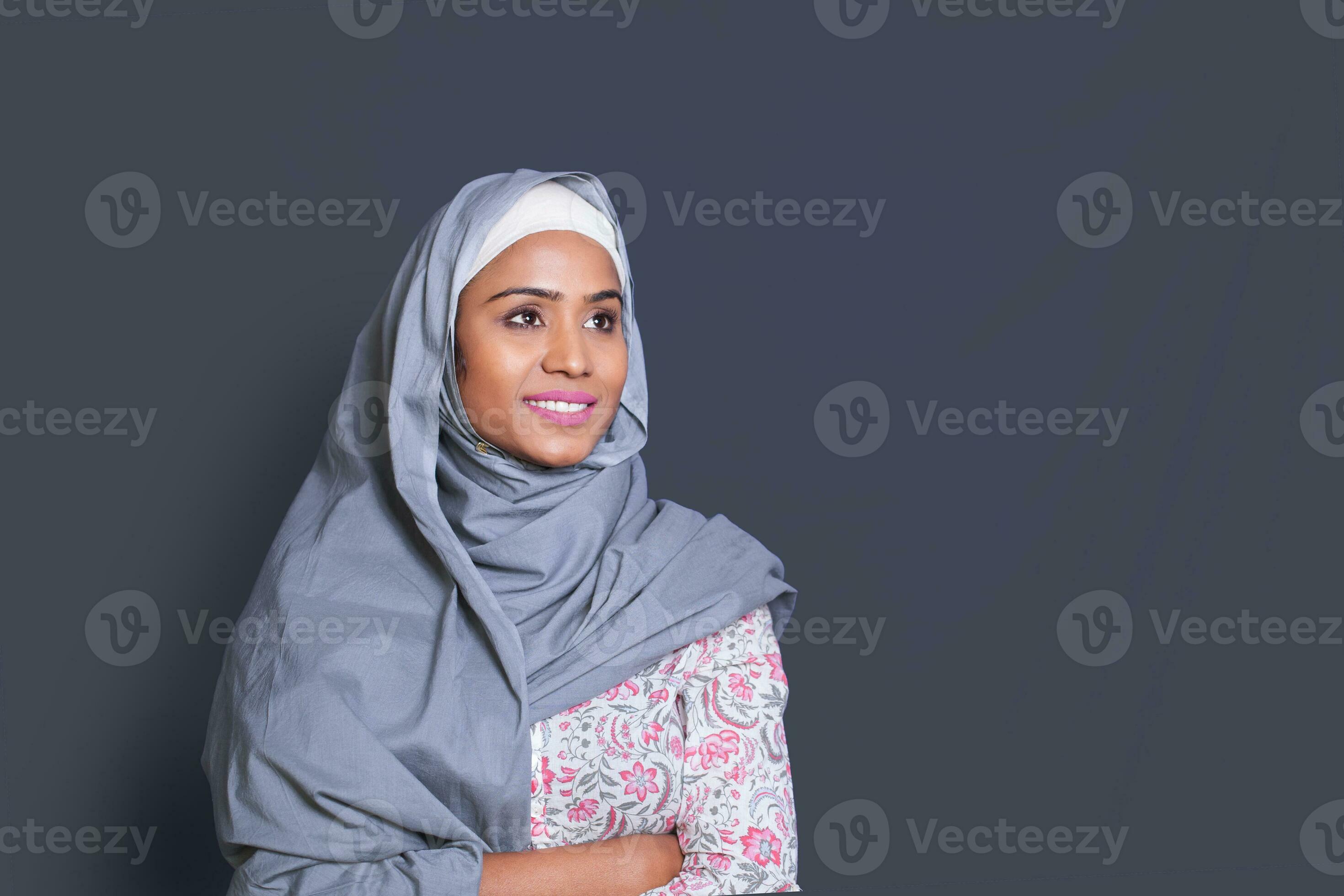 Beautiful muslim Indian young woman wearing hijab standing over grey studio background with arms ...