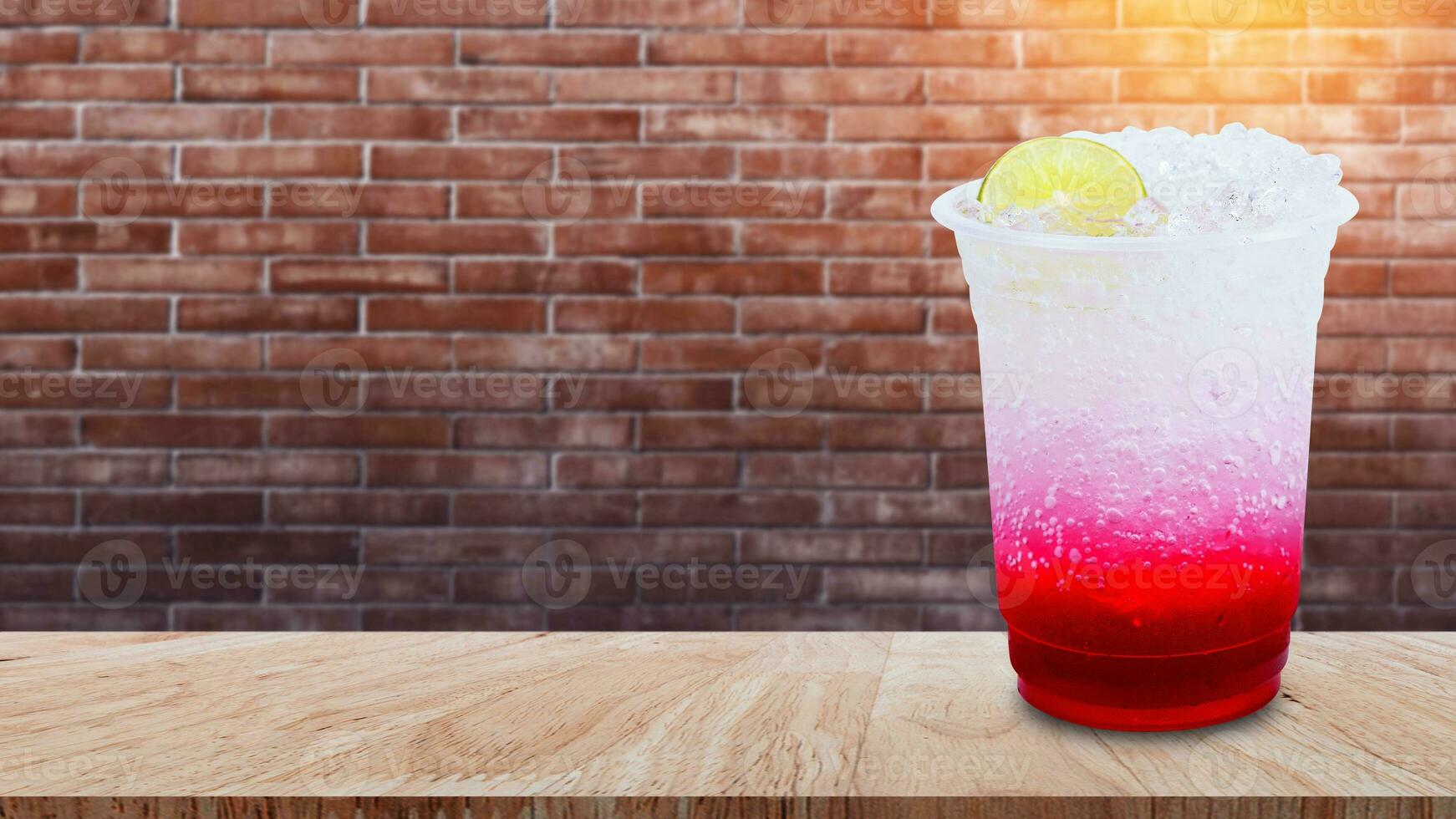 Italian soda made from fruit syrup drink mix in plastic cup on wooden table. Lemon, Red cocktail ...