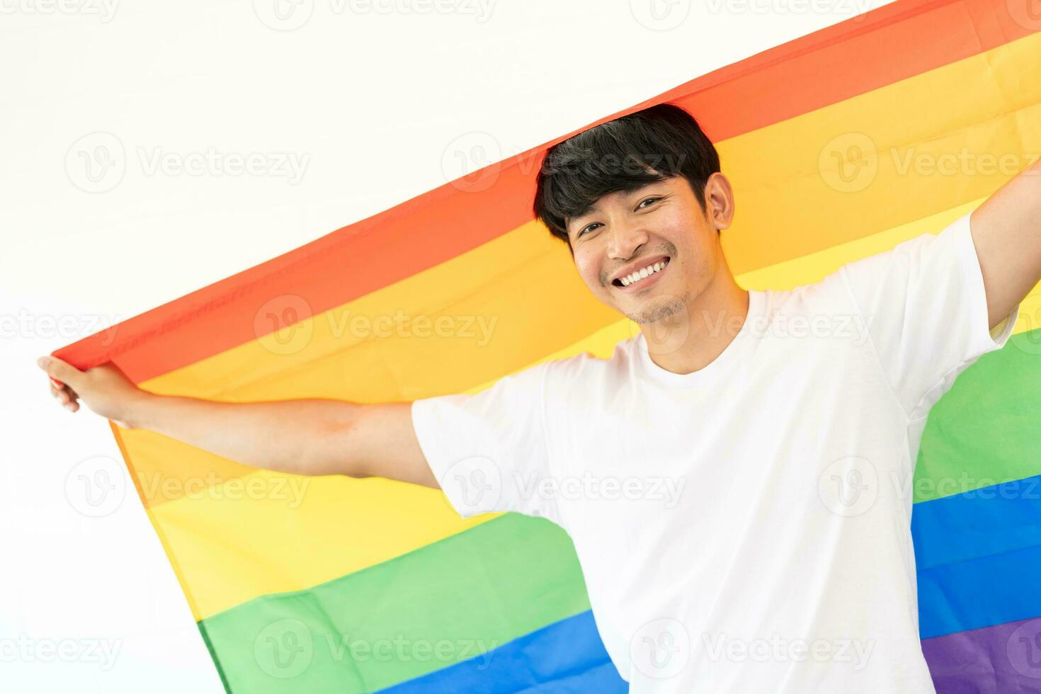 Cheerful young man wrapped in rainbow flag enjoying isolated on white ...