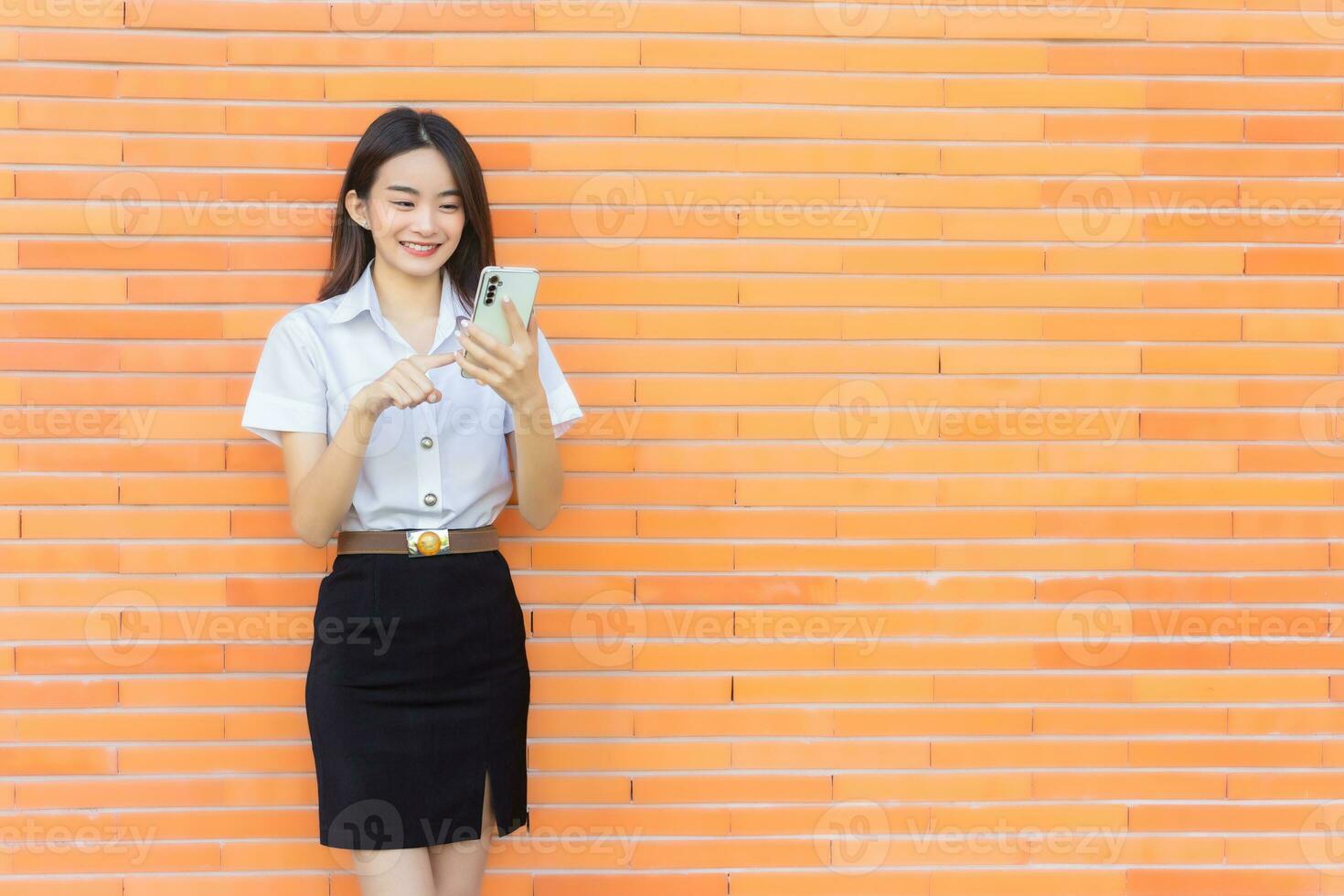 Portrait young Asian beautiful and pretty Thai girl student in uniform while using smartphone ...